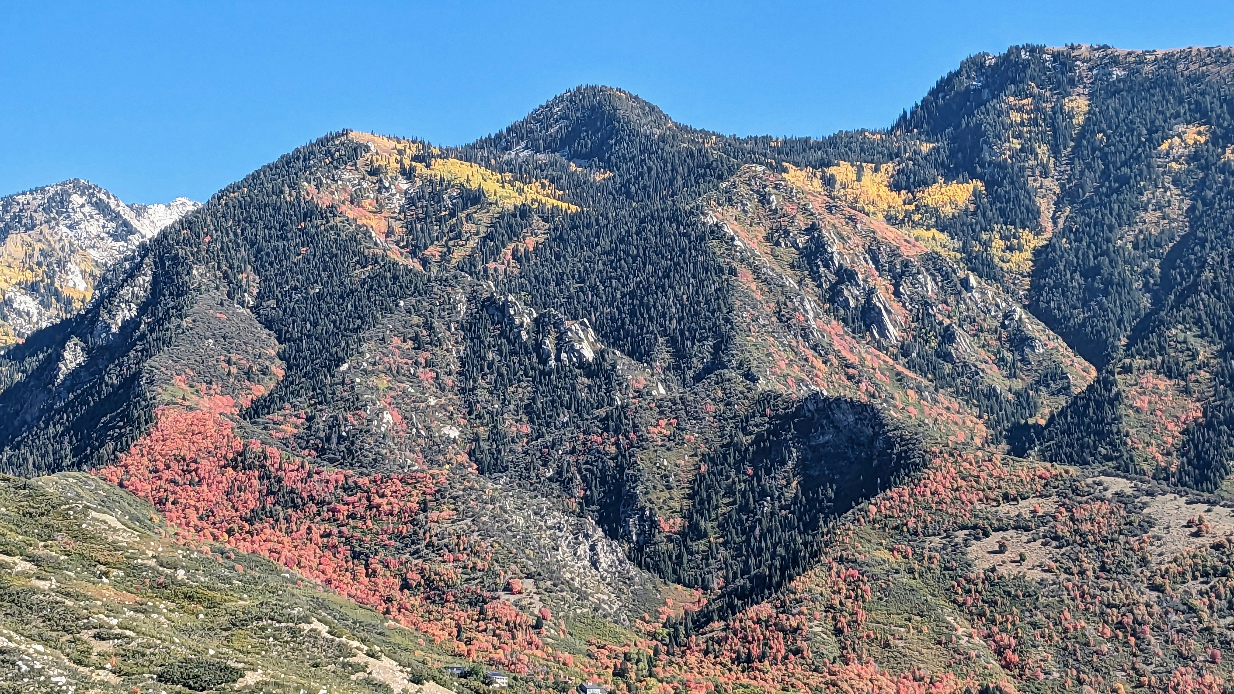 Mountain range with patches of red and yellow autumn foliage under a clear blue sky.