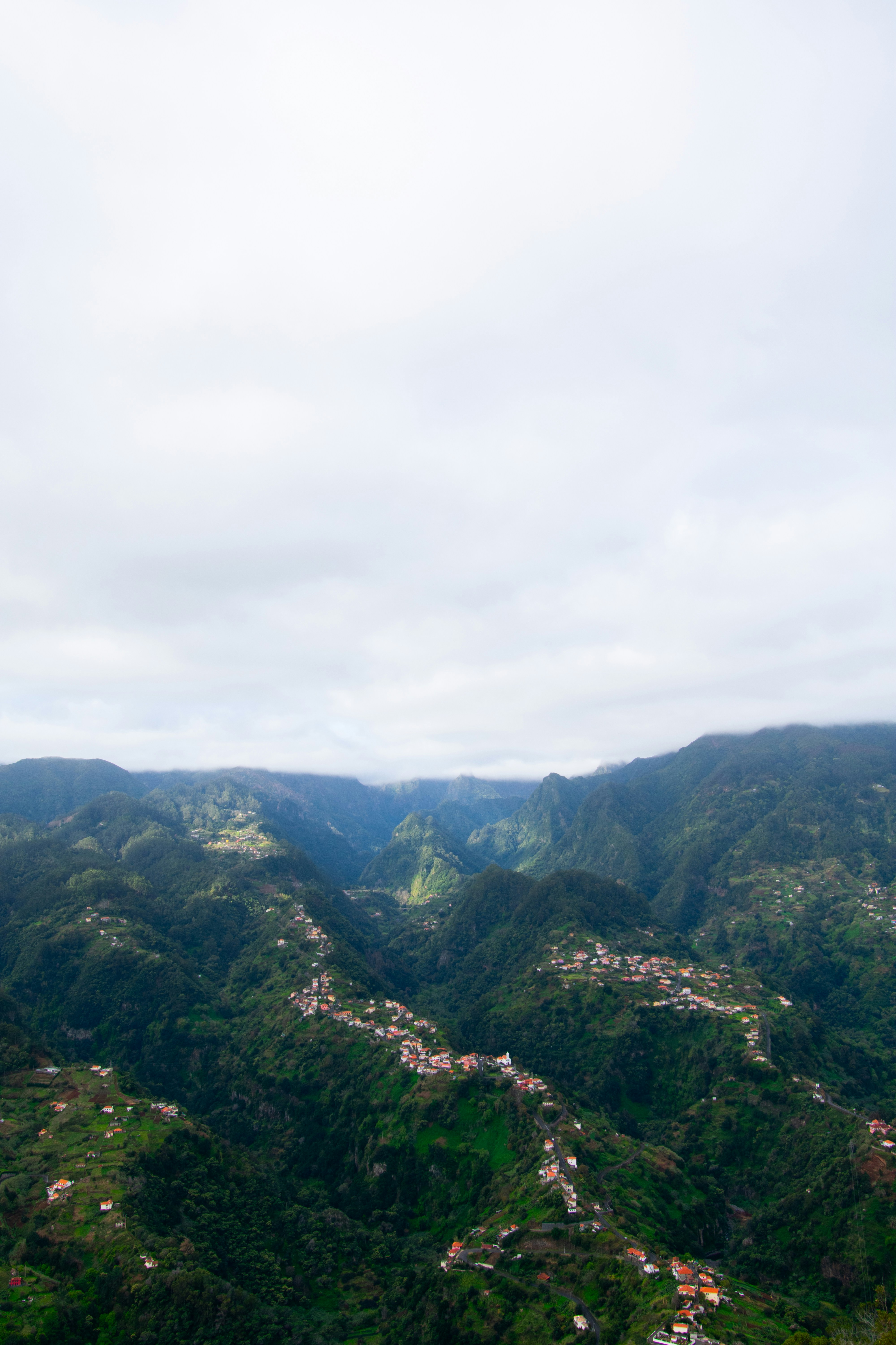 Lush green valleys interspersed with quaint villages under a soft, cloudy sky. The terrain showcases the harmony between nature and human habitation.