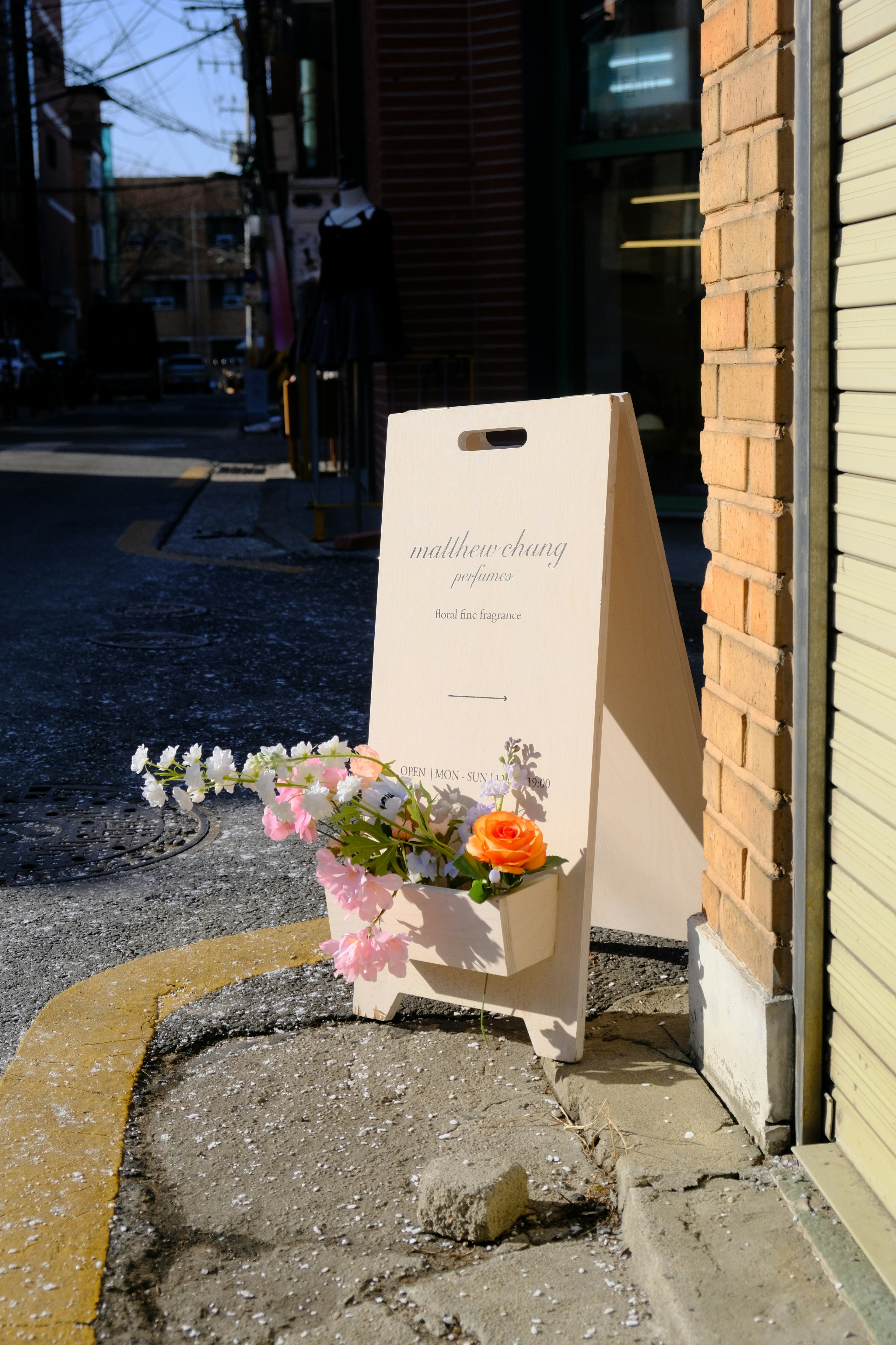 Floral tribute leaning against a boutique sign on a sunlit urban sidewalk