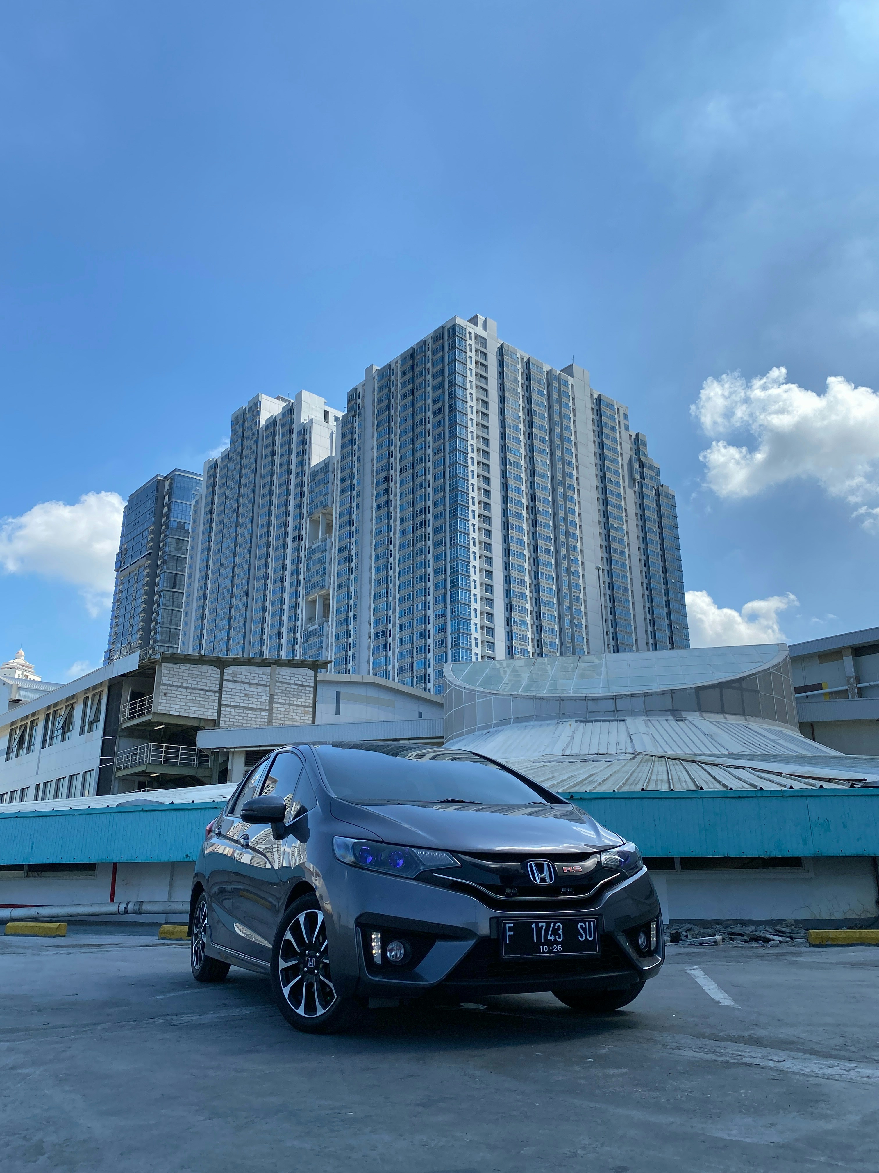 Rooftop Rendezvous: A Honda Hatchback Framed by a Glass-Soaked City Skyline