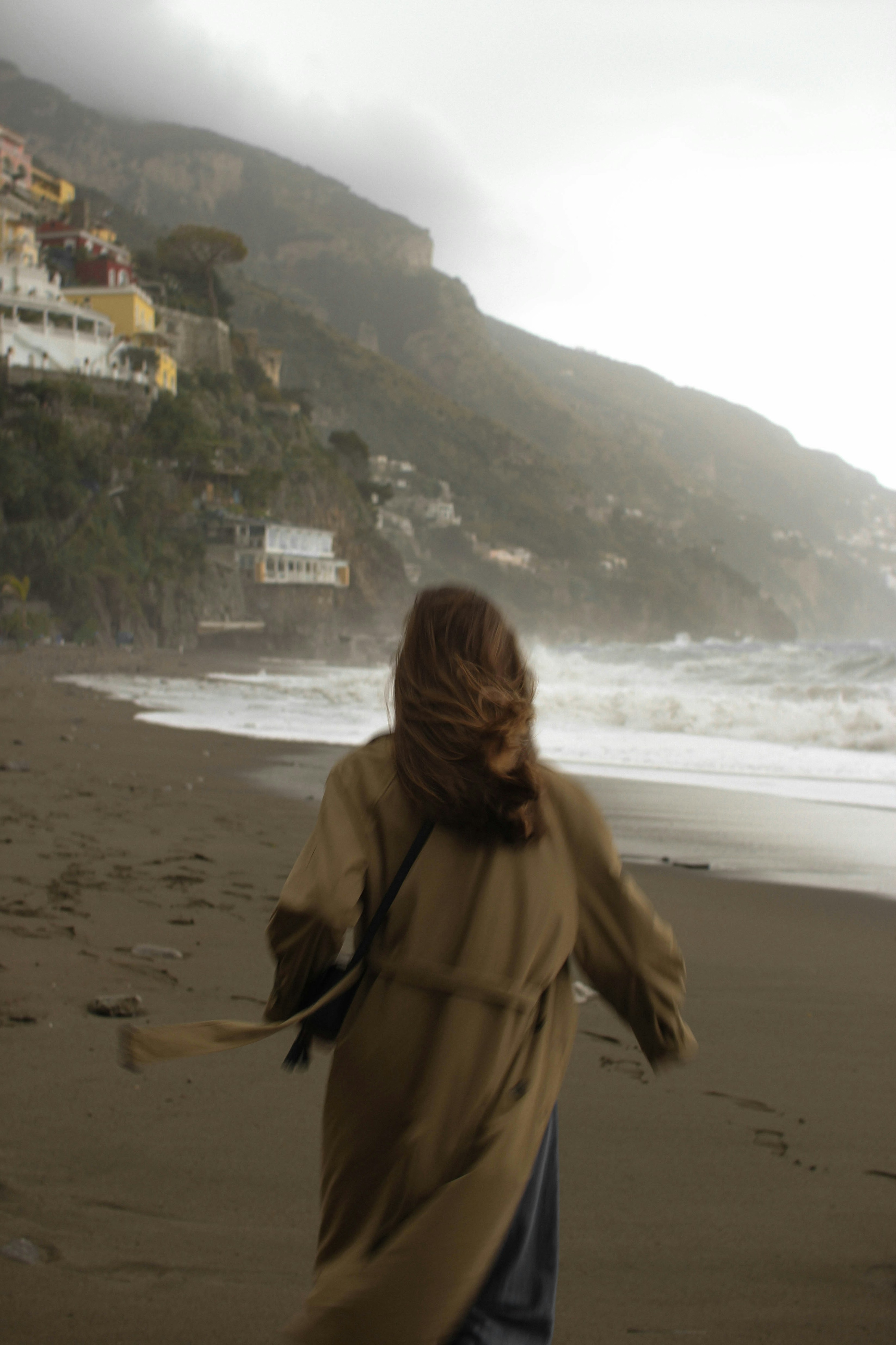 Toward the Mist: A Beige-Coat Figure Treads a Cliffside Beach