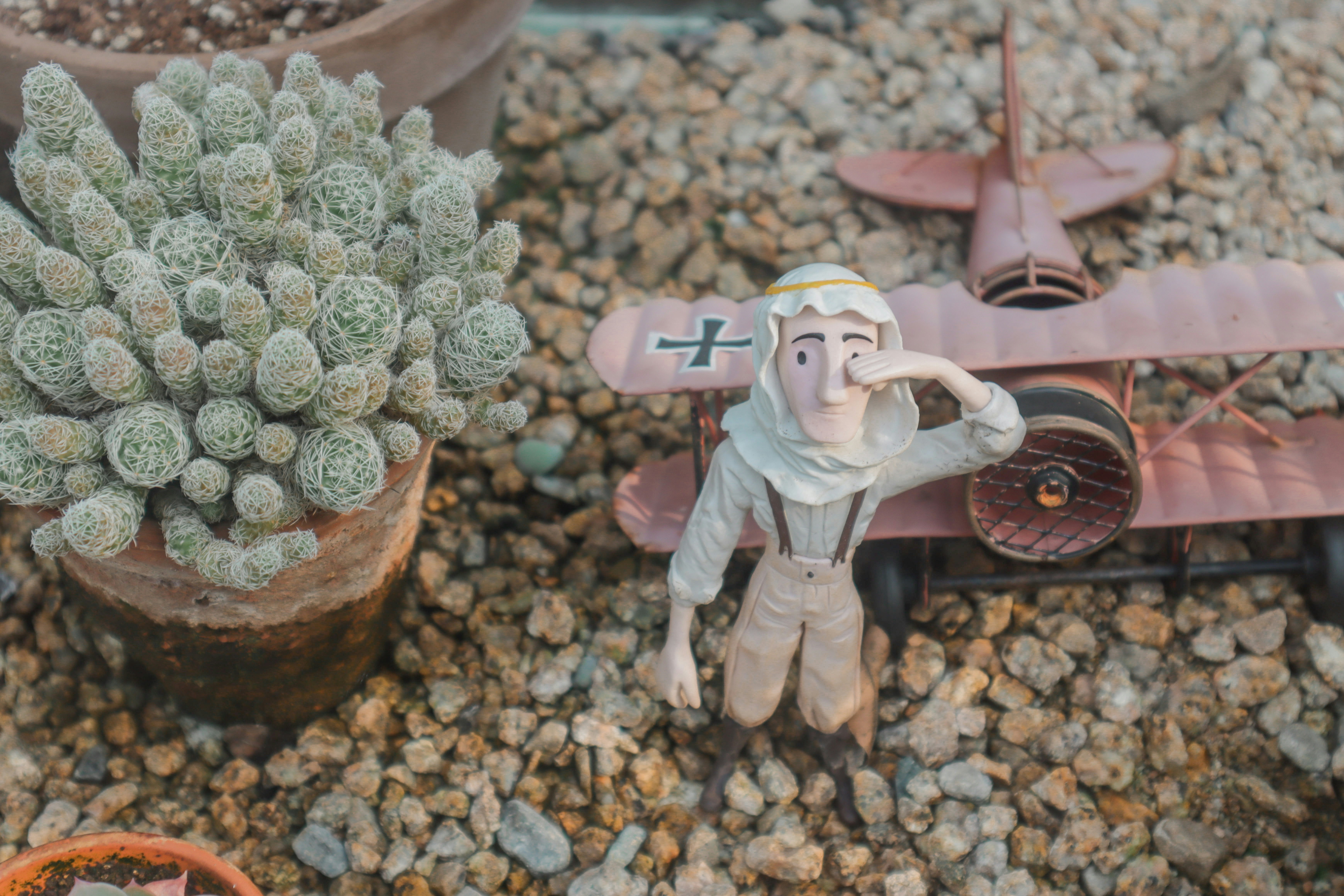 Saluting Miniature Pilot by a Rusty Toy Plane in a Pebble Garden