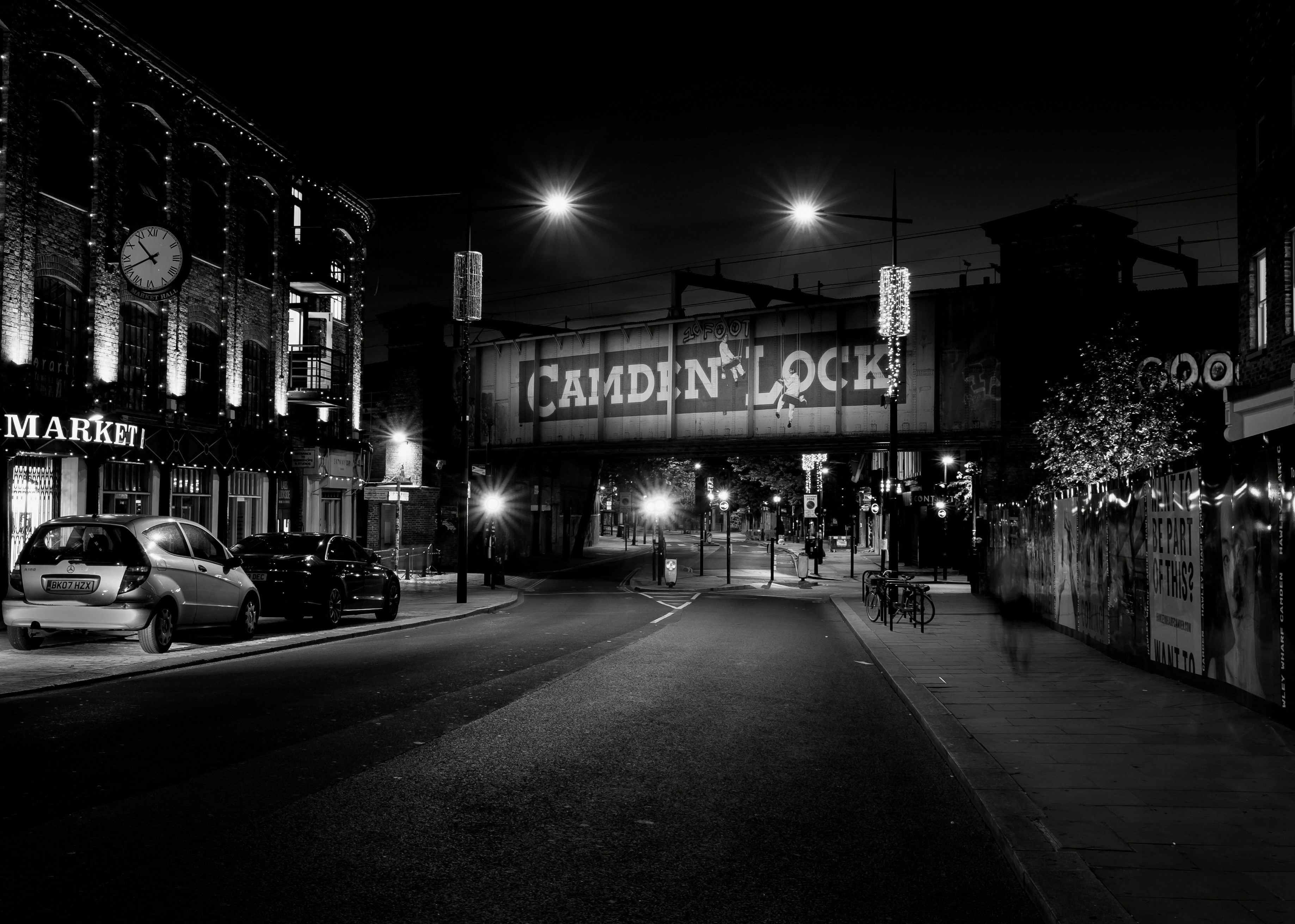 Black and white view of Camden Lock bridge at night, illuminated by streetlights with a vintage ambiance.