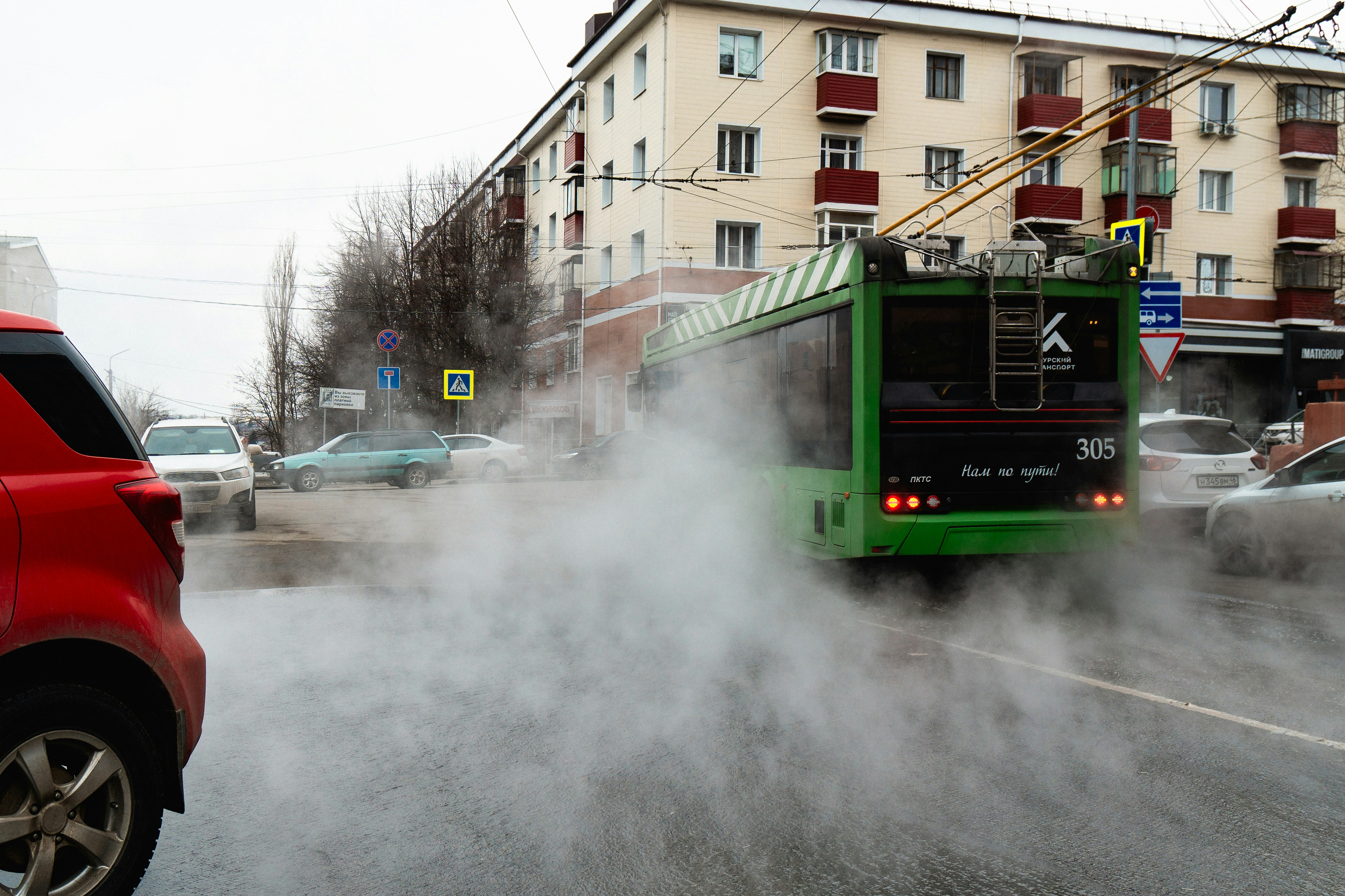 Emerald Tram Through Steam at a Rain-Misted City Crossroads