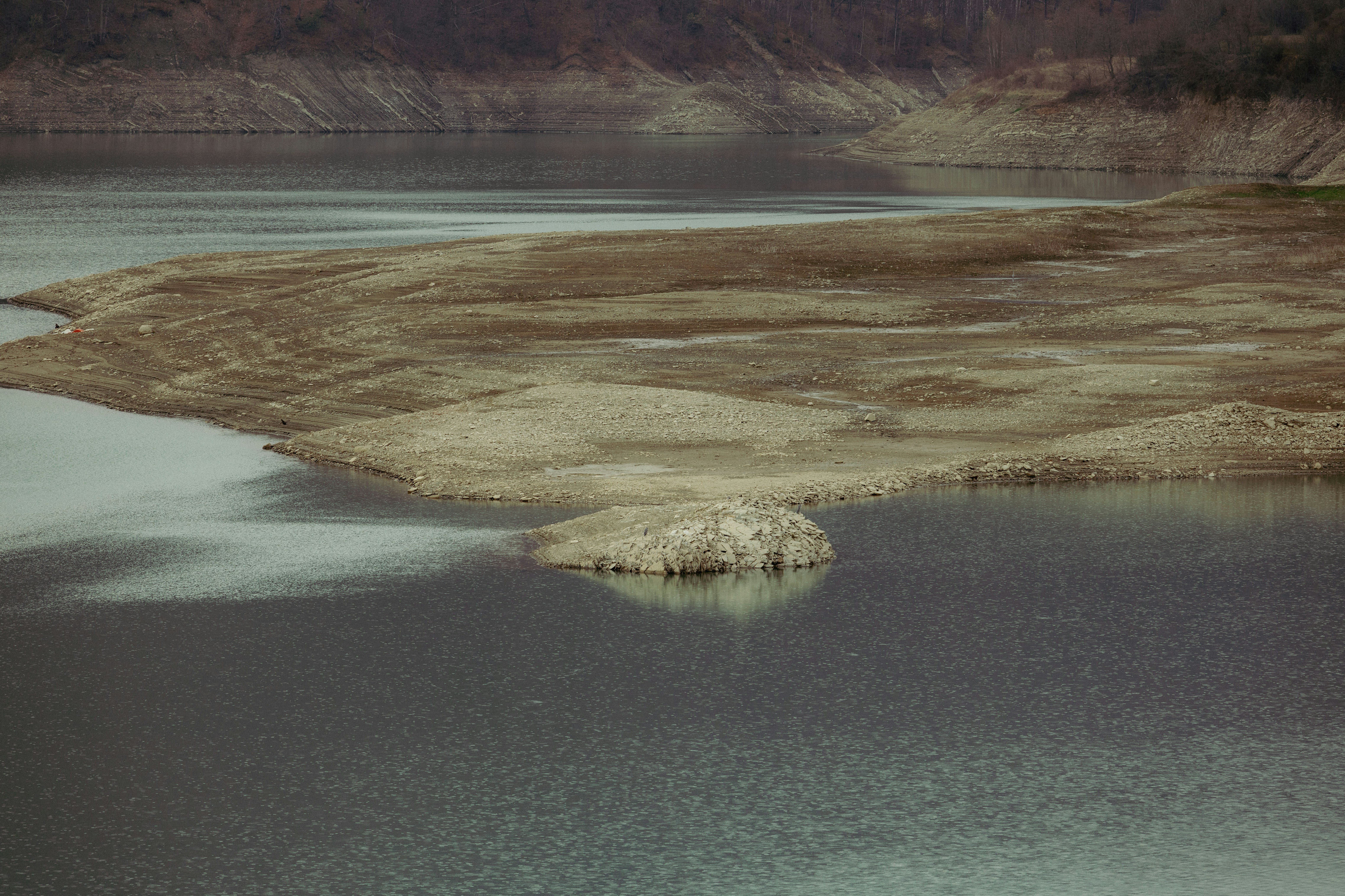 The Quiet Islet: Mud-Bronze Shallows Framing a Glassy Lake
