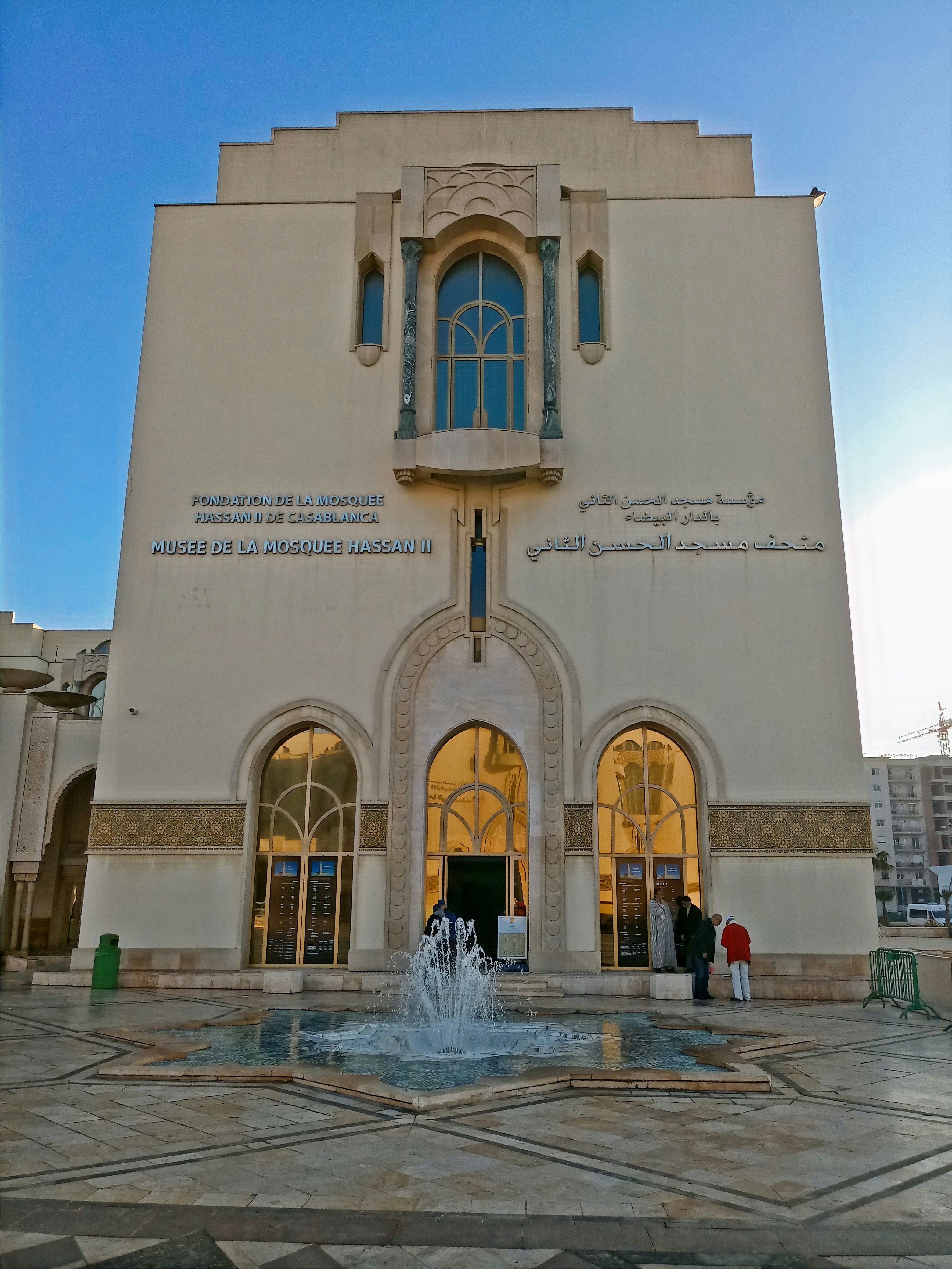 Elegant facade with arched windows and central fountain under a clear blue sky.