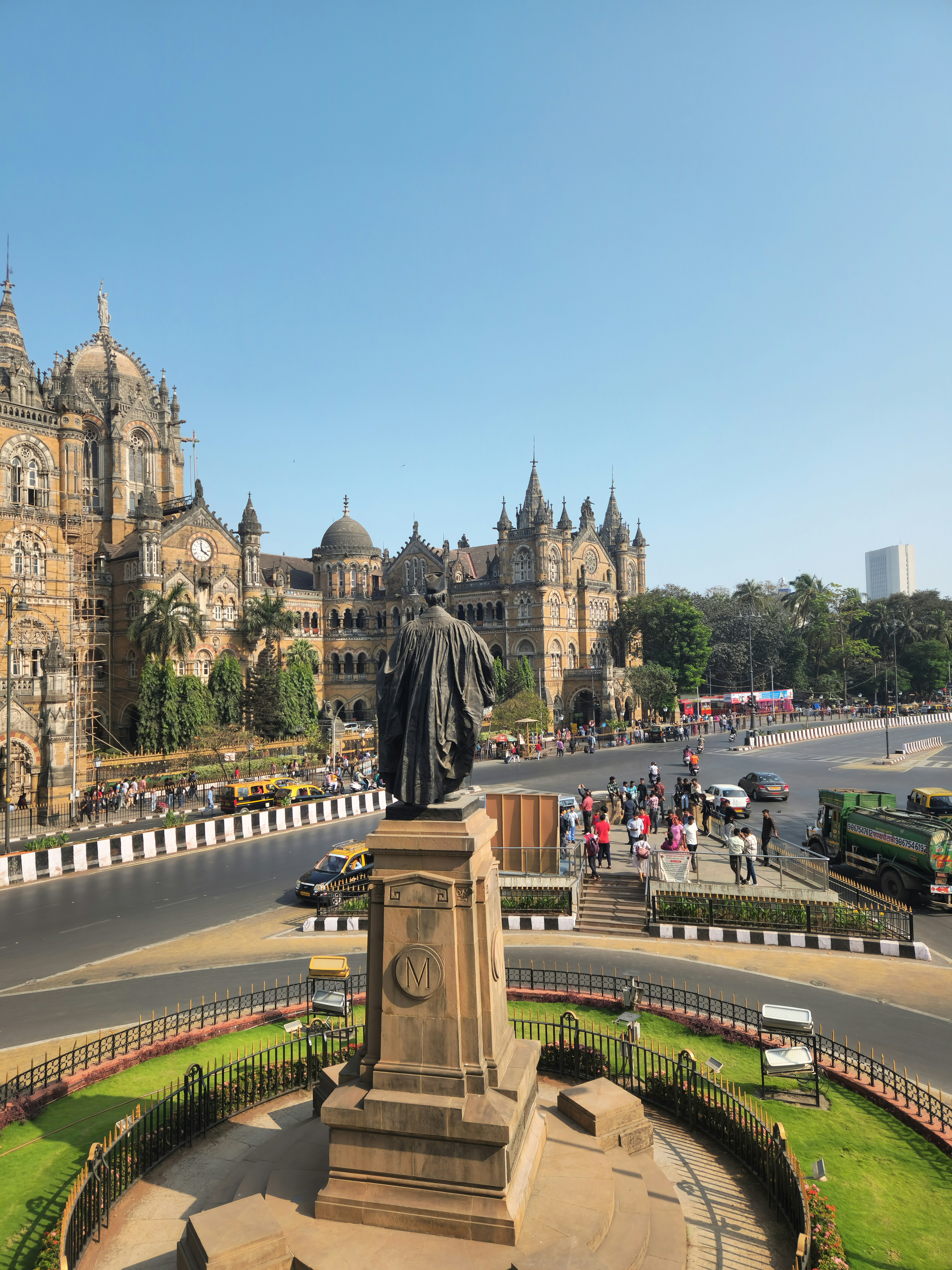 Pedestal Sentinel: Bronze statue guarding a circular garden before Mumbai's Gothic campus arcades