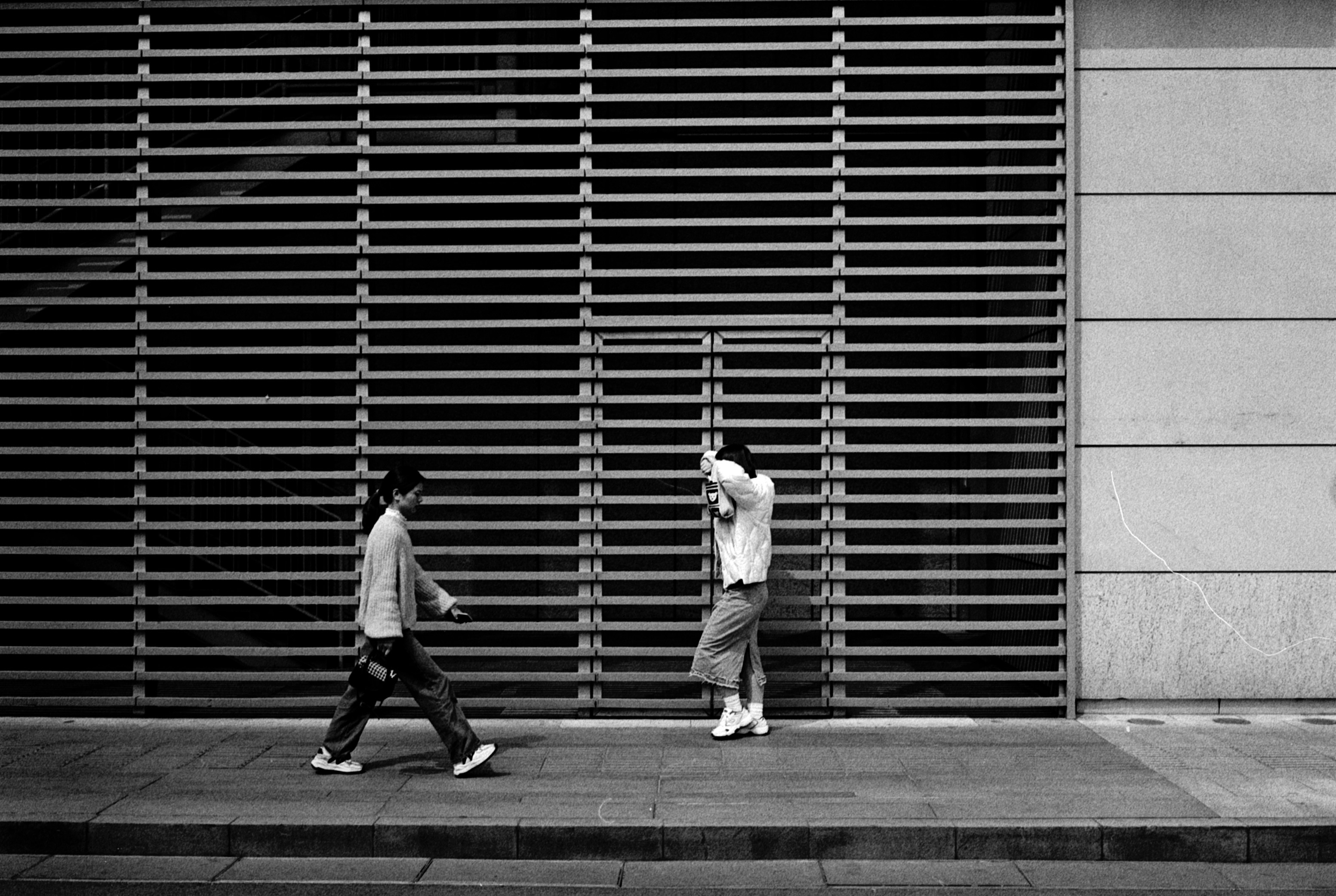 Two people walking in front of a large, horizontal louvered facade.