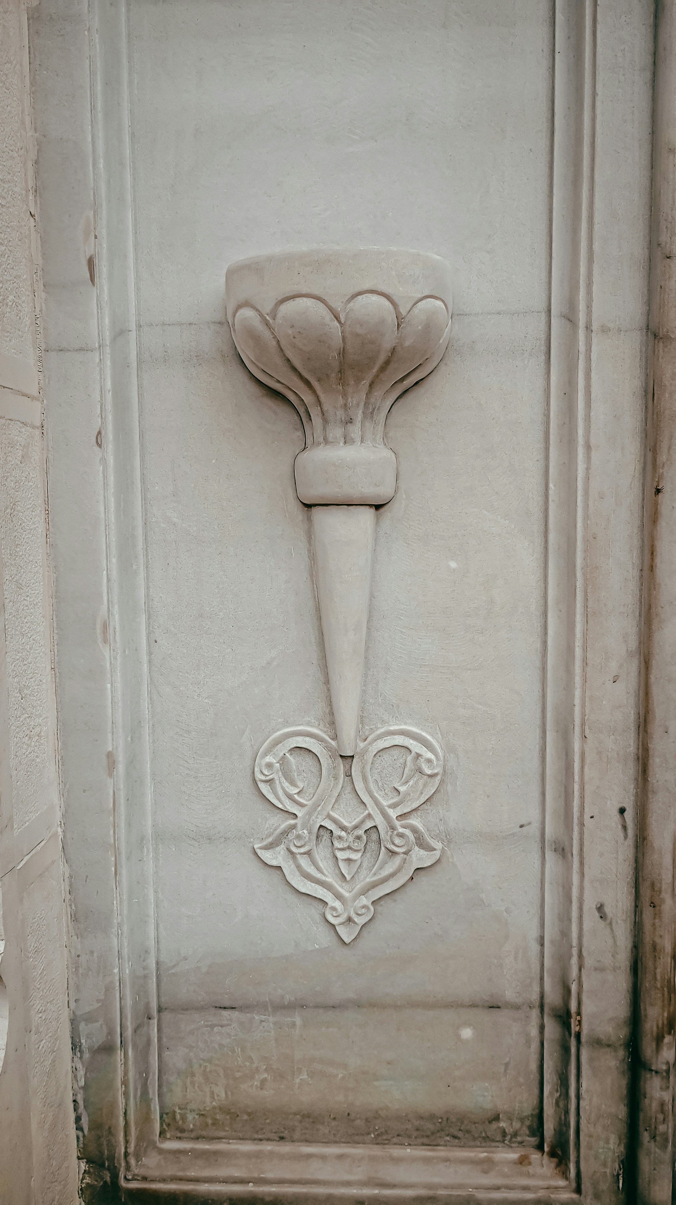 Marble relief carving of a stylized torch centerpiece on a paneled wall.