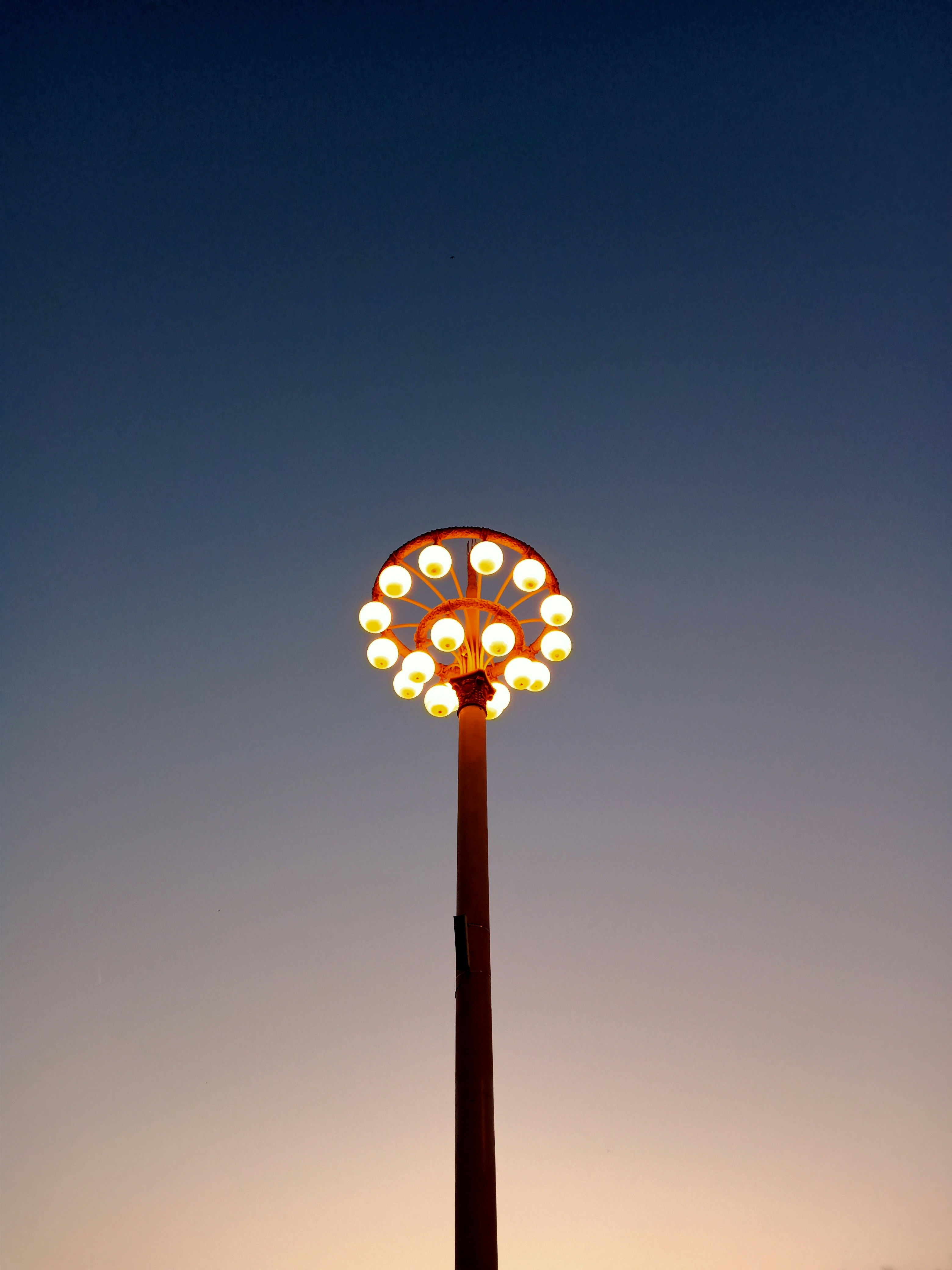 Photograph of a solitary streetlamp with a halo of bulbs against a gradient dusk sky.