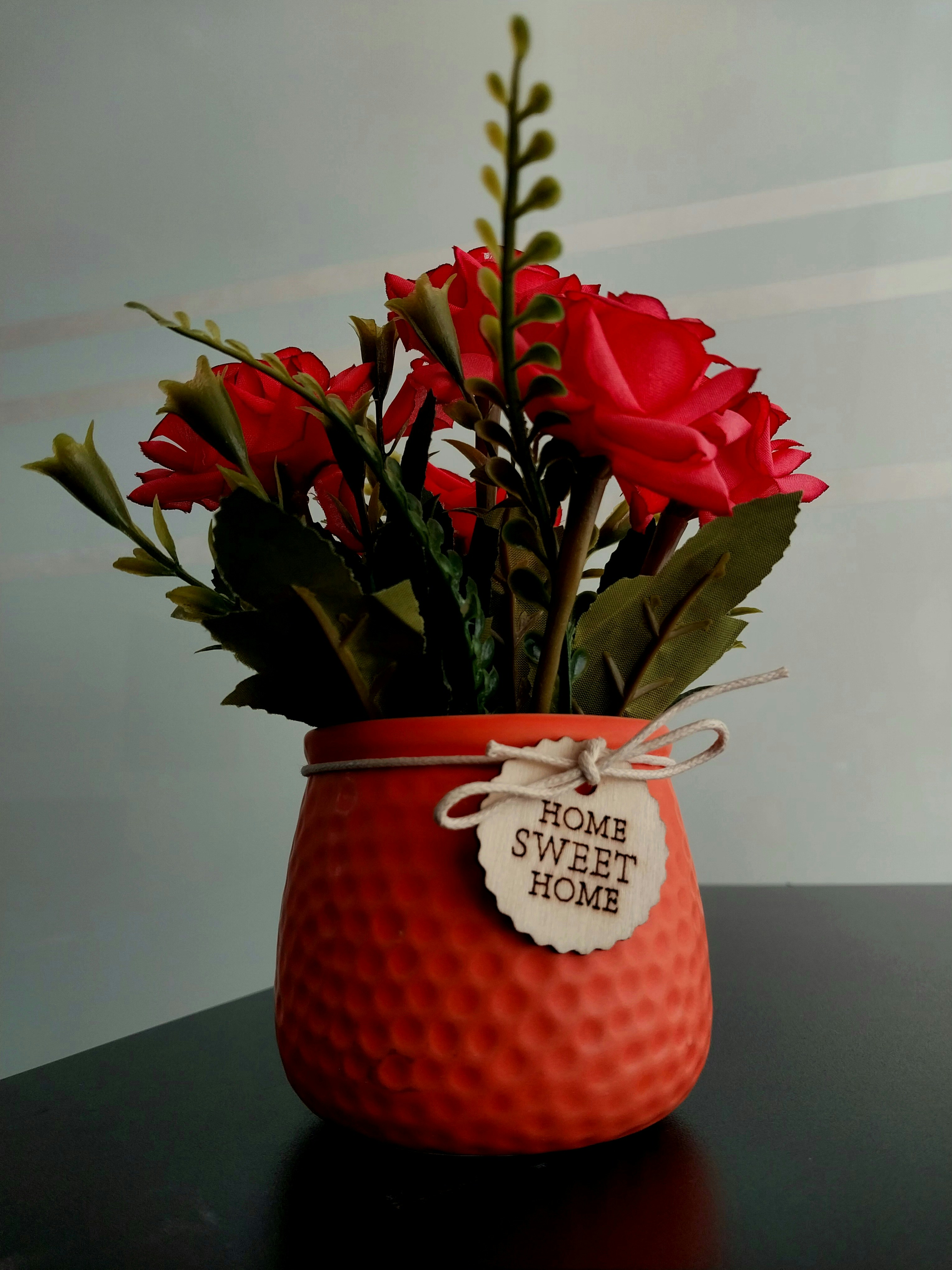 Red roses in a textured red vase that reads "Home Sweet Home"