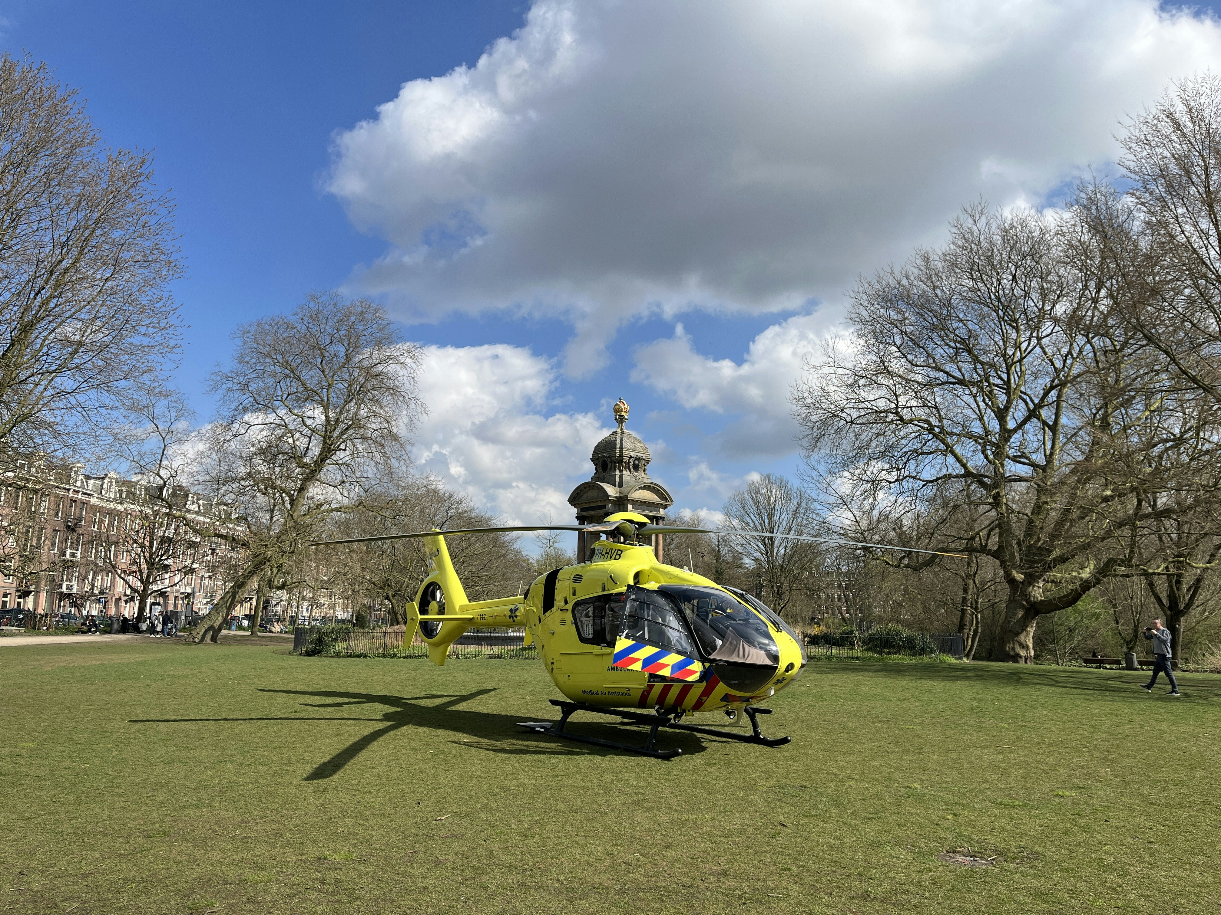 Sunlit Yellow Rescue Helicopter Anchors a Park Lawn Under a Cloud-Dotted Sky