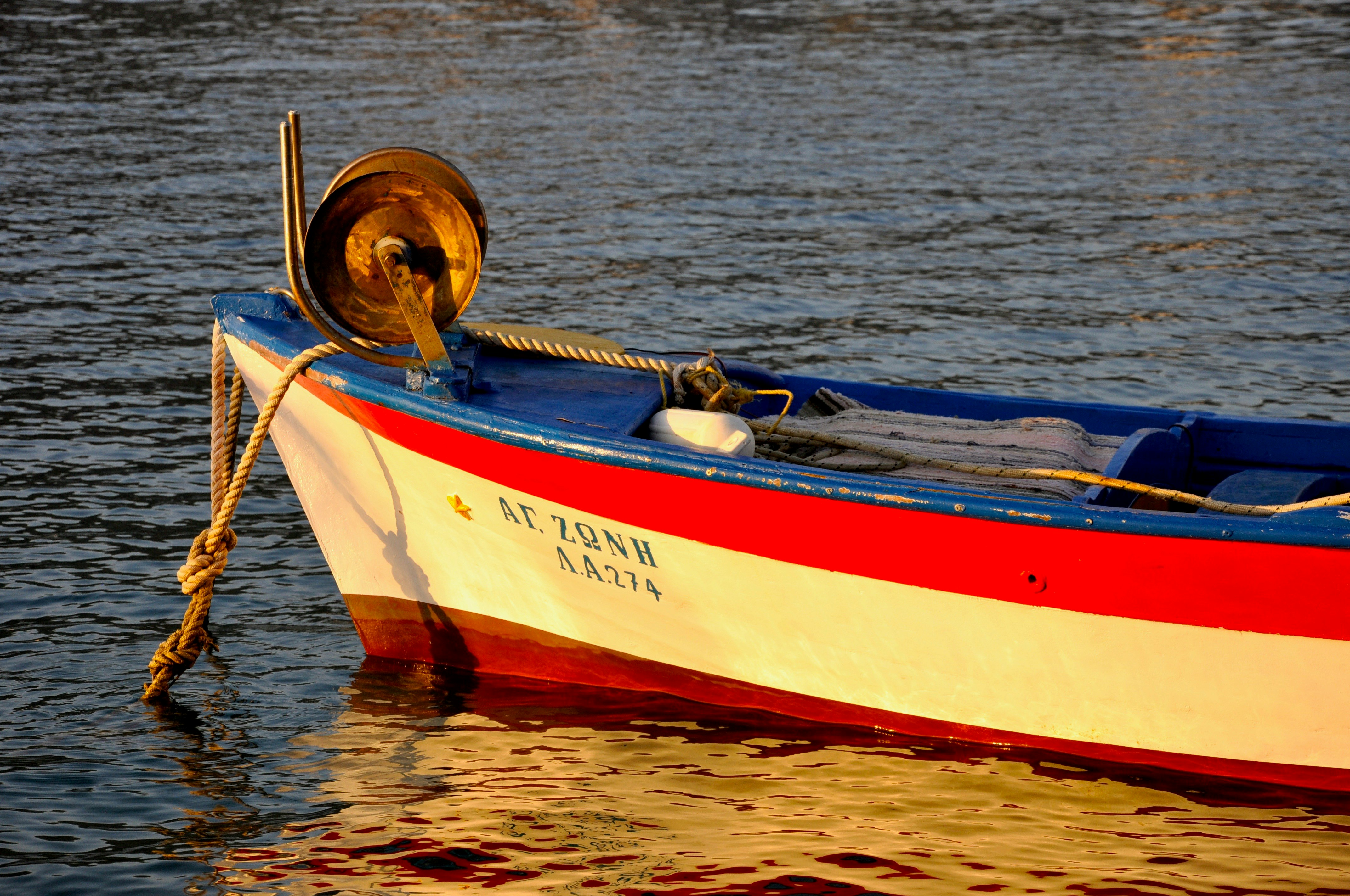 Red, white, and blue boat gently floating on sunlit water with a golden hue.