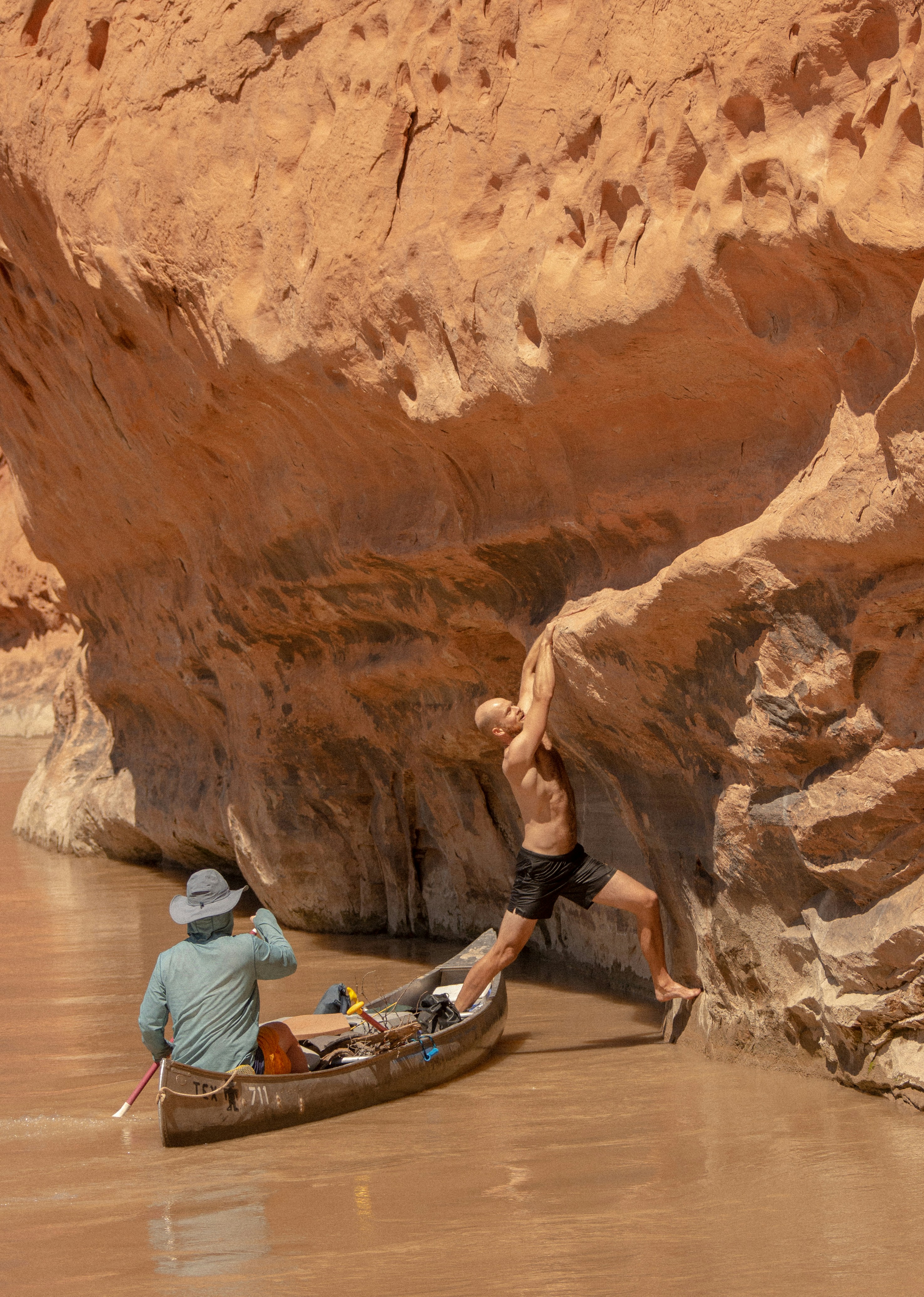 Climber's Bold Reach on a Sunlit Orange Cliff, Beside a Quiet Canoe