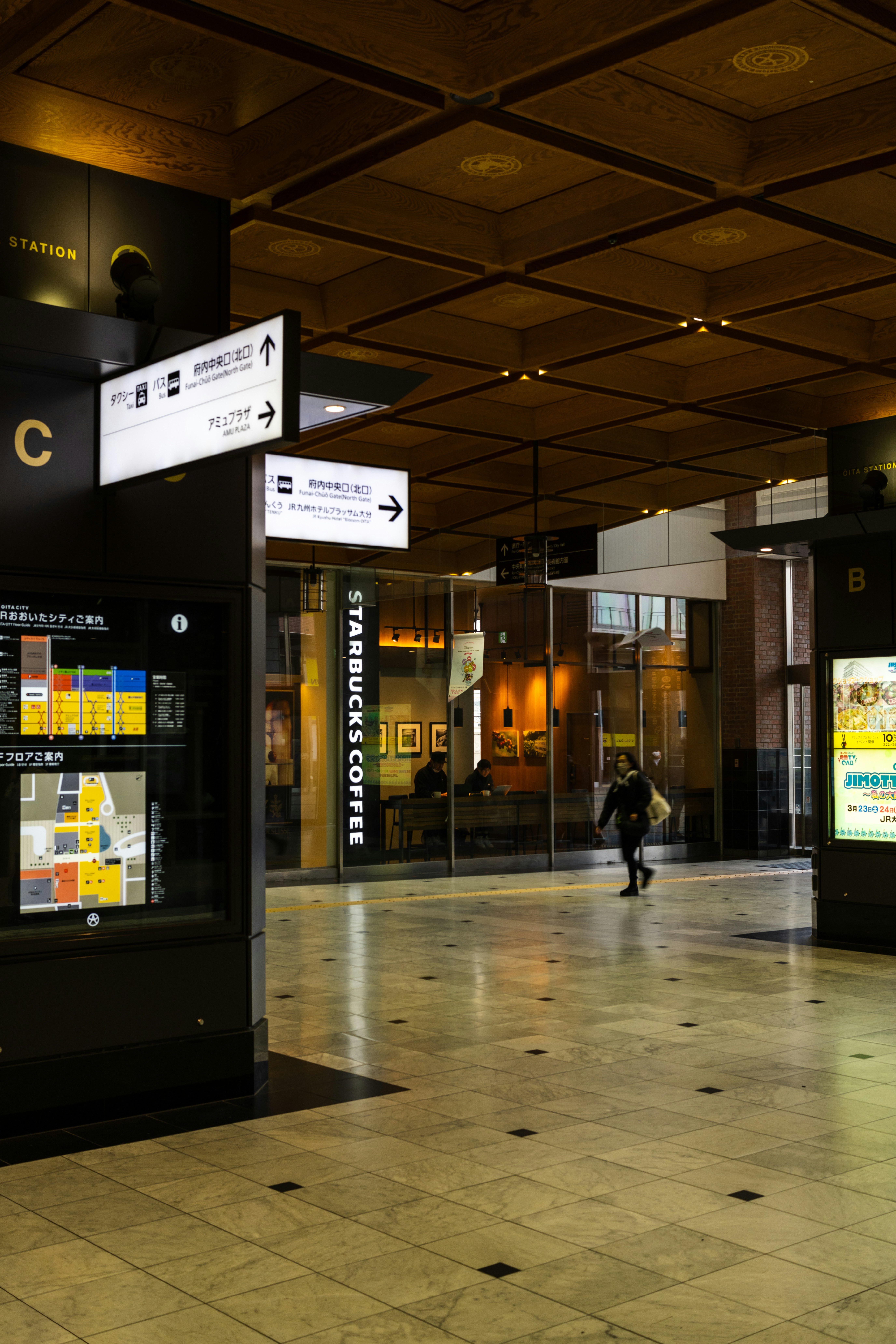 Transit Atrium at Dusk: A Solitary Traveler Beneath Warm Signage and Coffee Lights