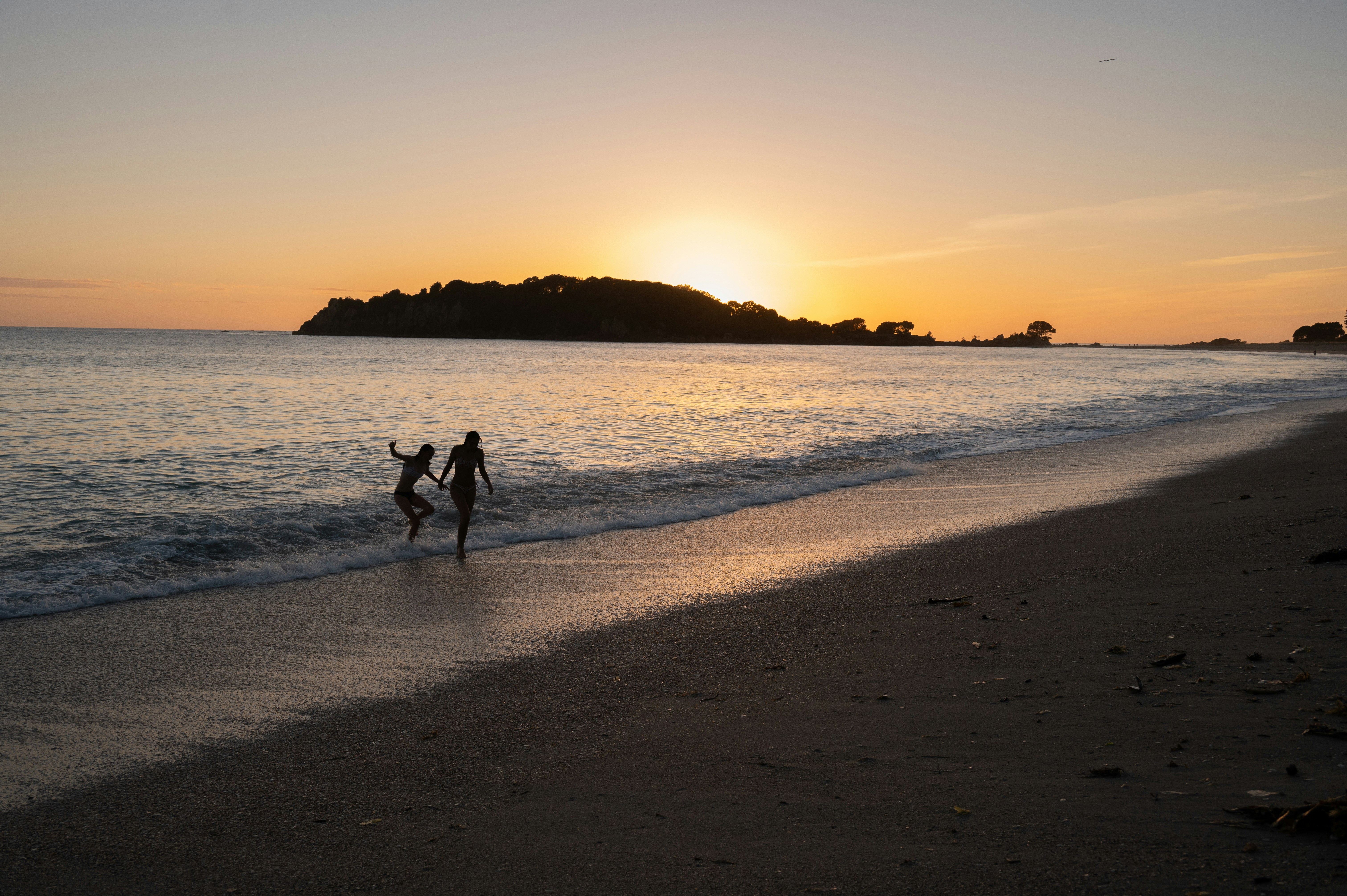 Silhouetted figures play in the surf at sunrise with an island in the distance.