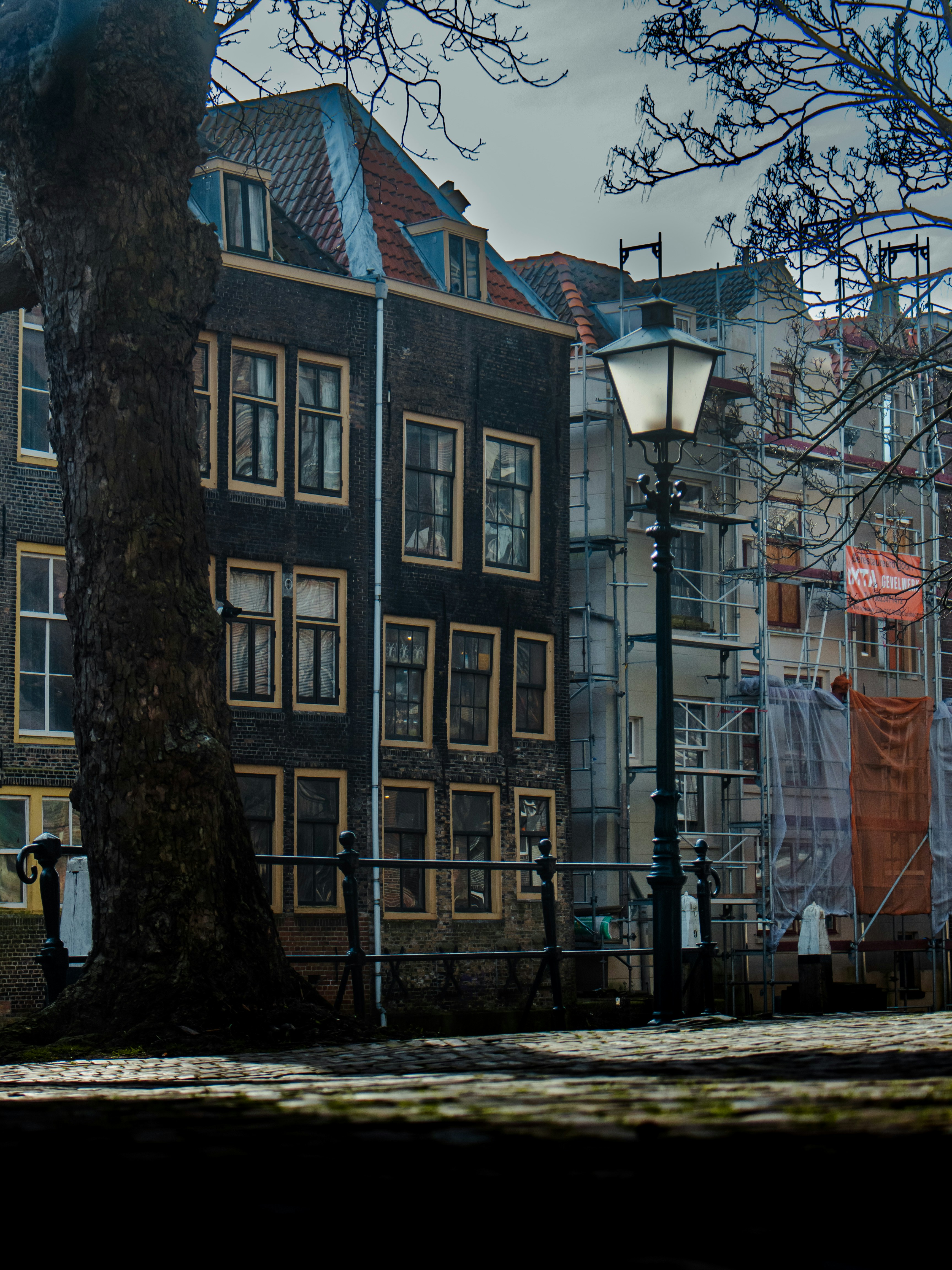 Lamppost Between Time: Historic Facades and Fresh Scaffolding on a Dutch Cobblestone Street