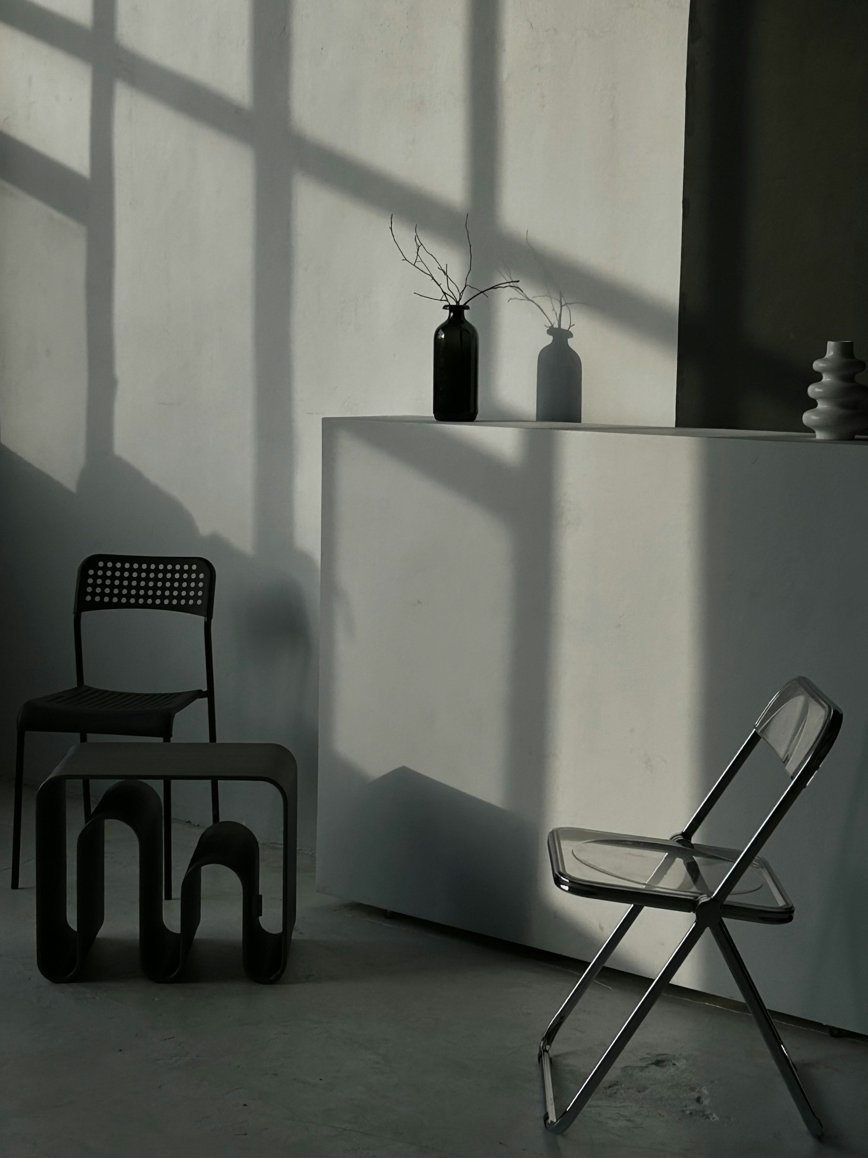 Sunlight casting geometric shadows over a minimalist interior with two chairs and a table.