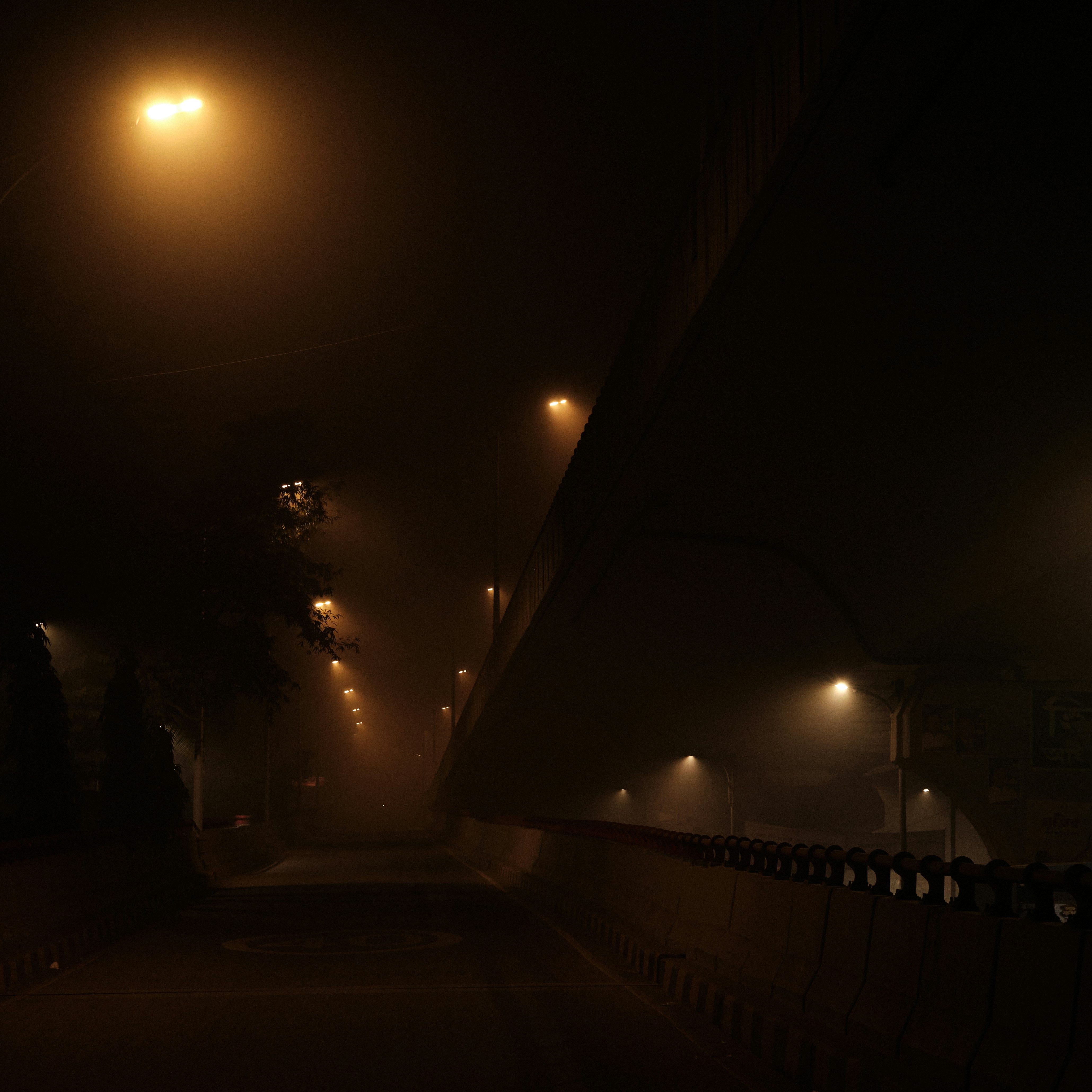 Dimly lit urban street shrouded in fog, illuminated by streetlights casting a mysterious glow.
