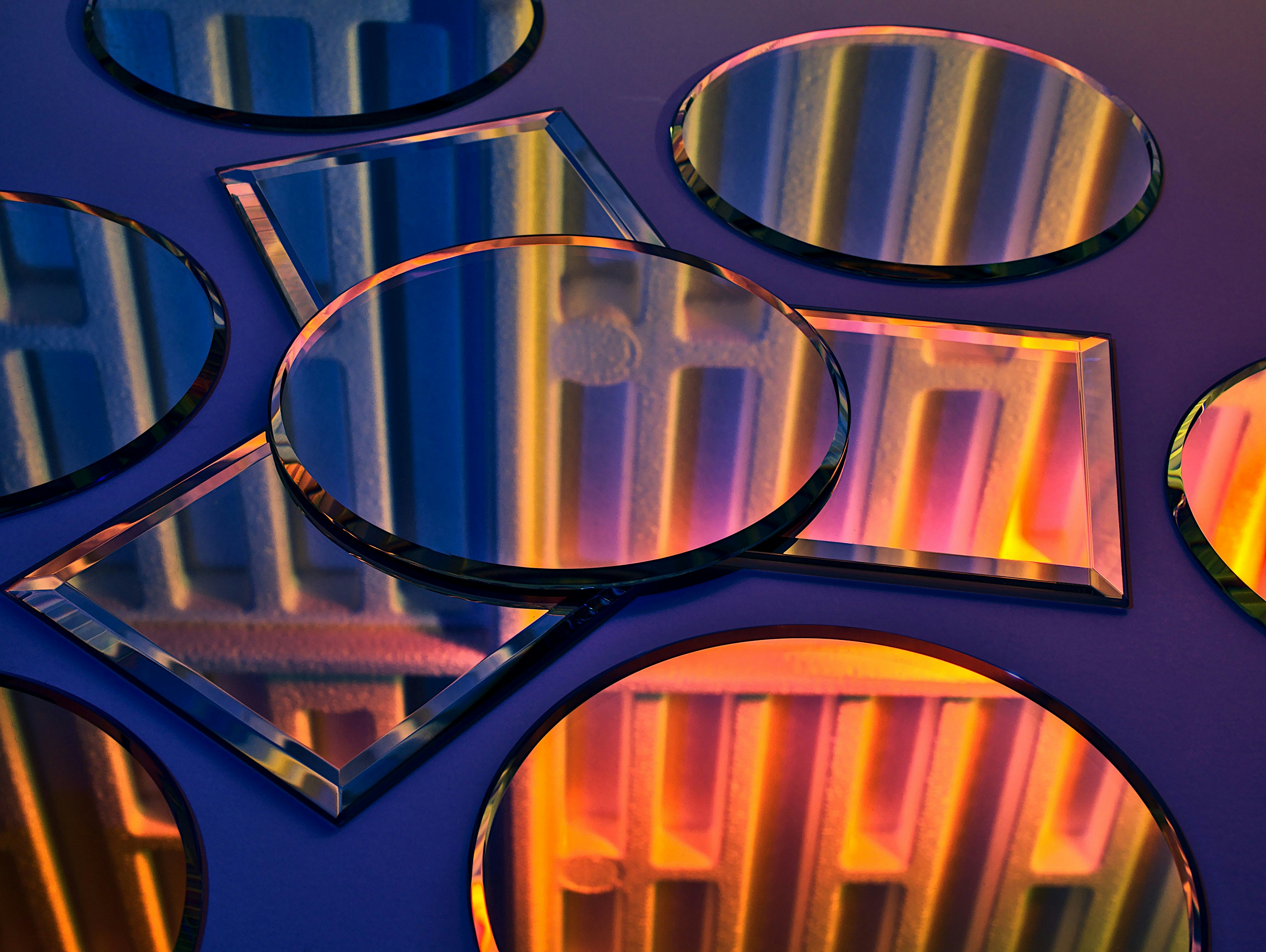 Abstract arrangement of circular and square mirrors reflecting vibrant neon stripes.