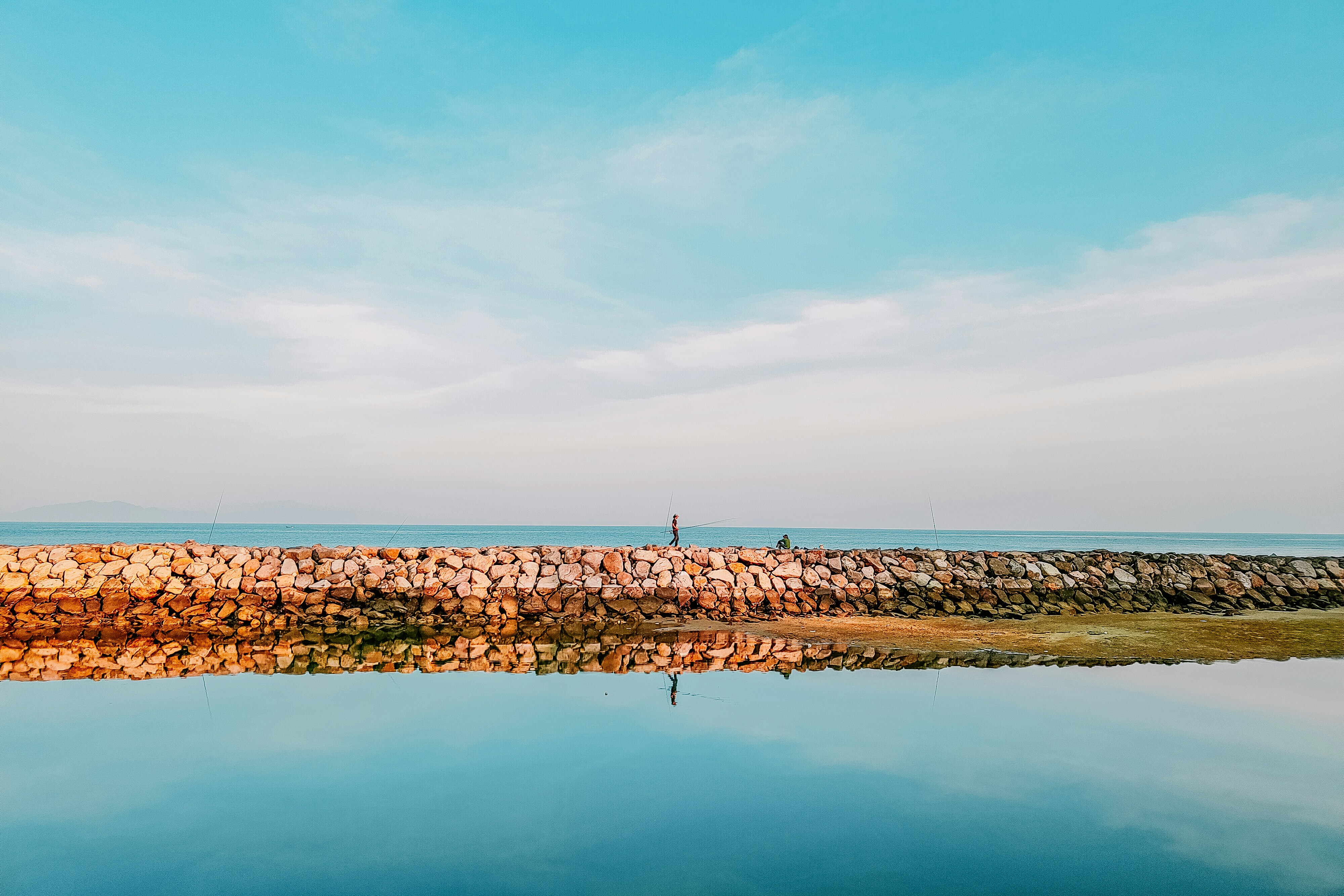 Rocky shoreline reflecting in calm waters under a clear blue sky.