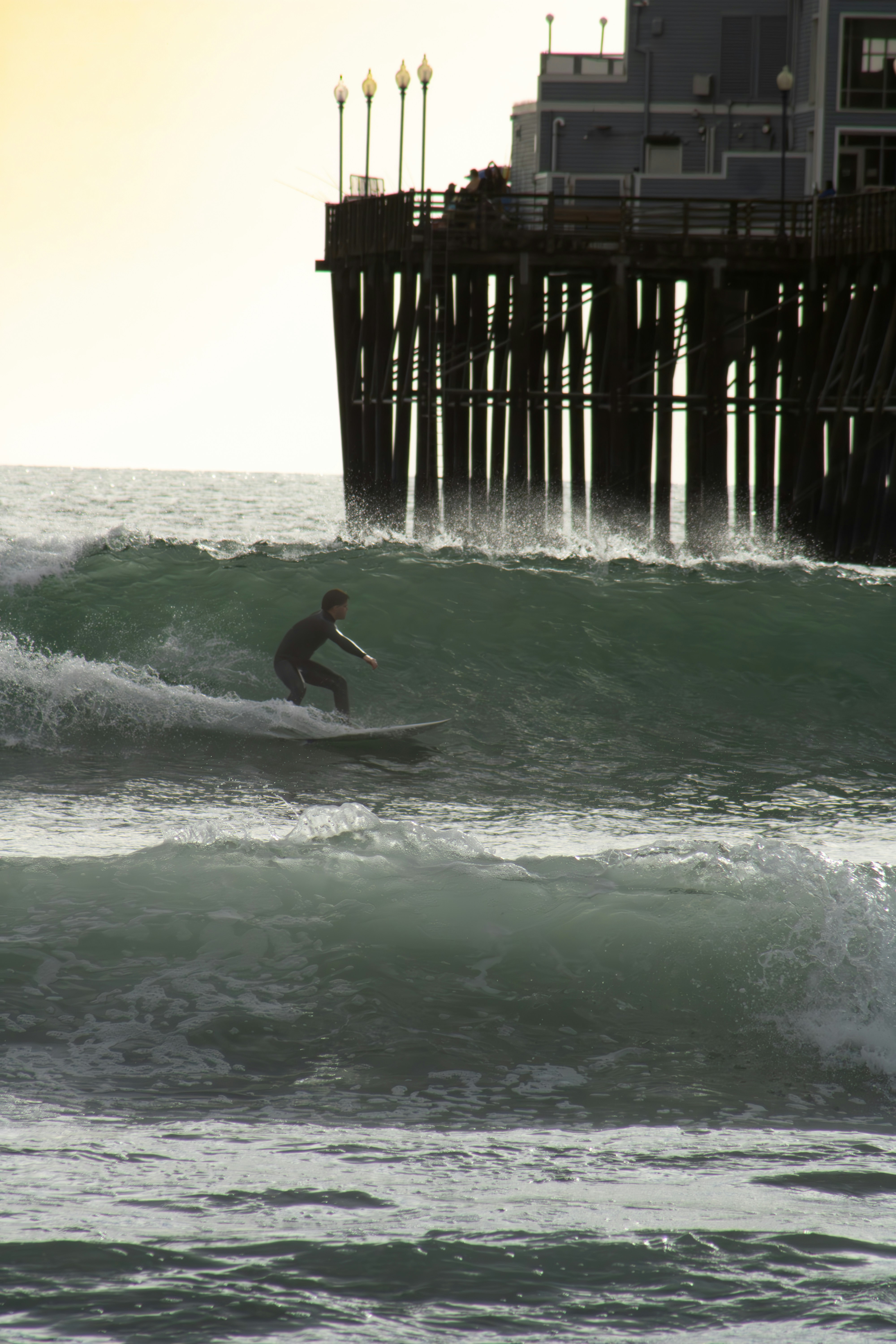 Surfer Tracing a Crest as the Pier Stands Sentry