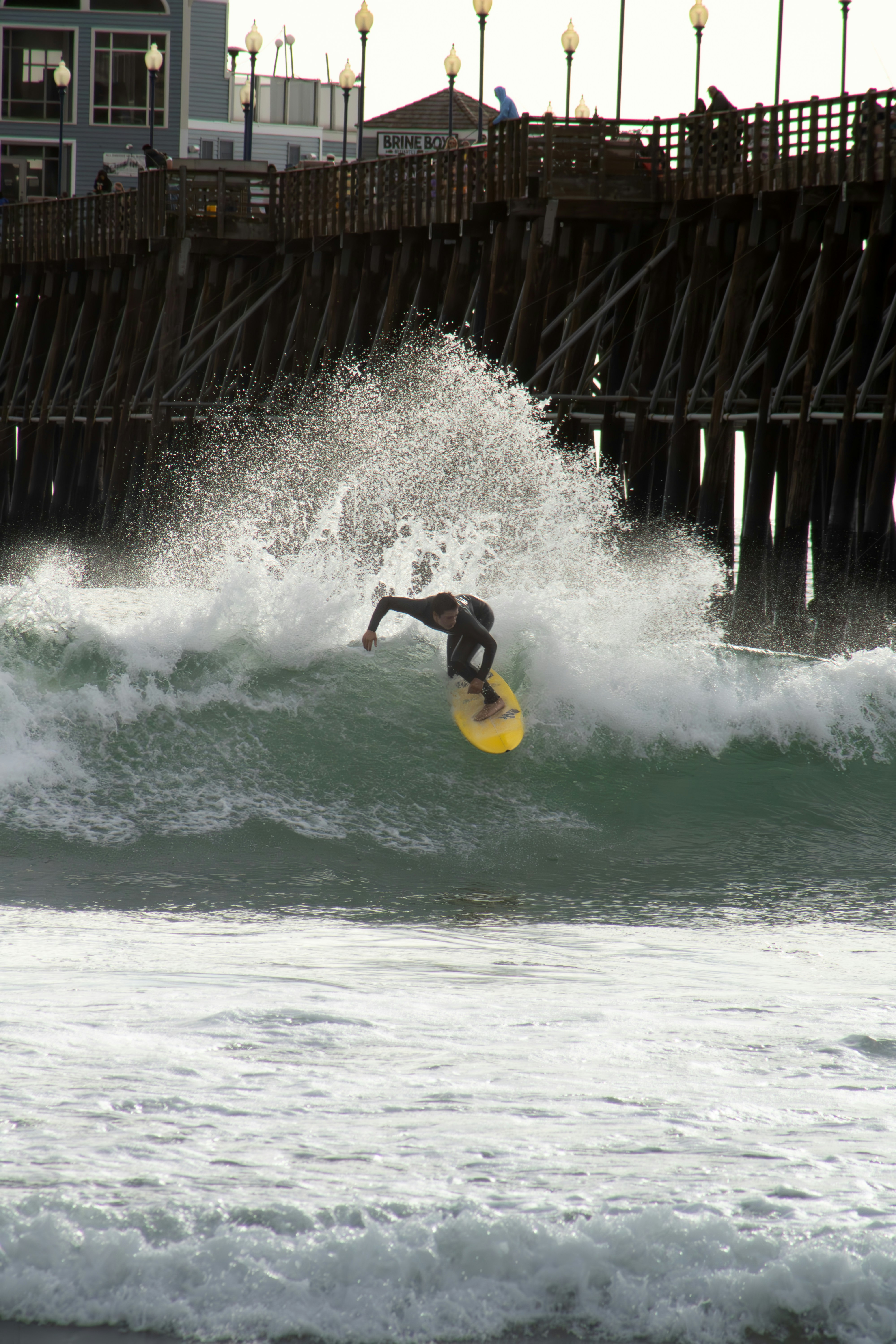 Pier-side Crest: Carving a Yellow Surfboard Through Hollow Spray