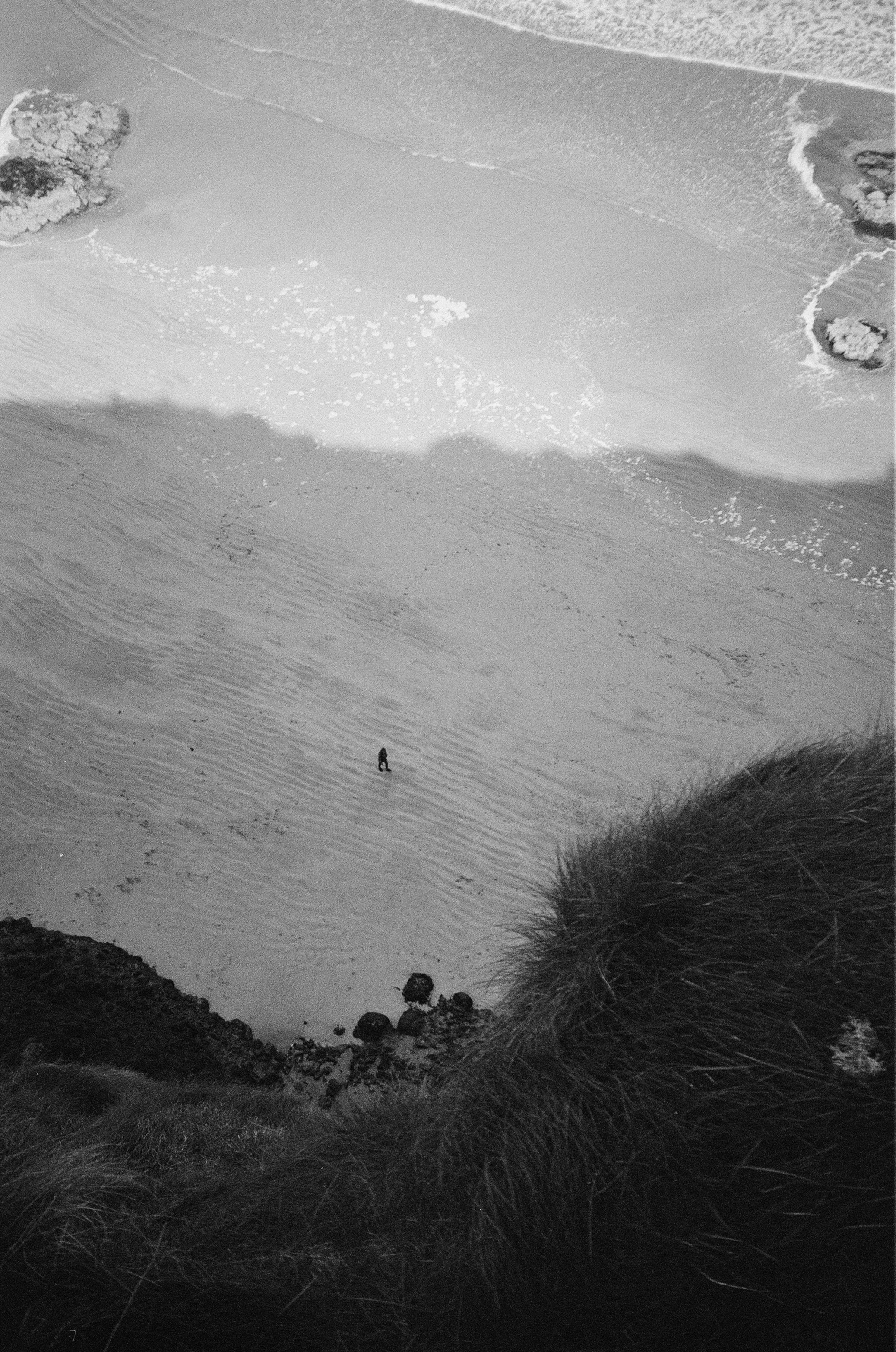 A film photo looking down onto a lone walker on a beach