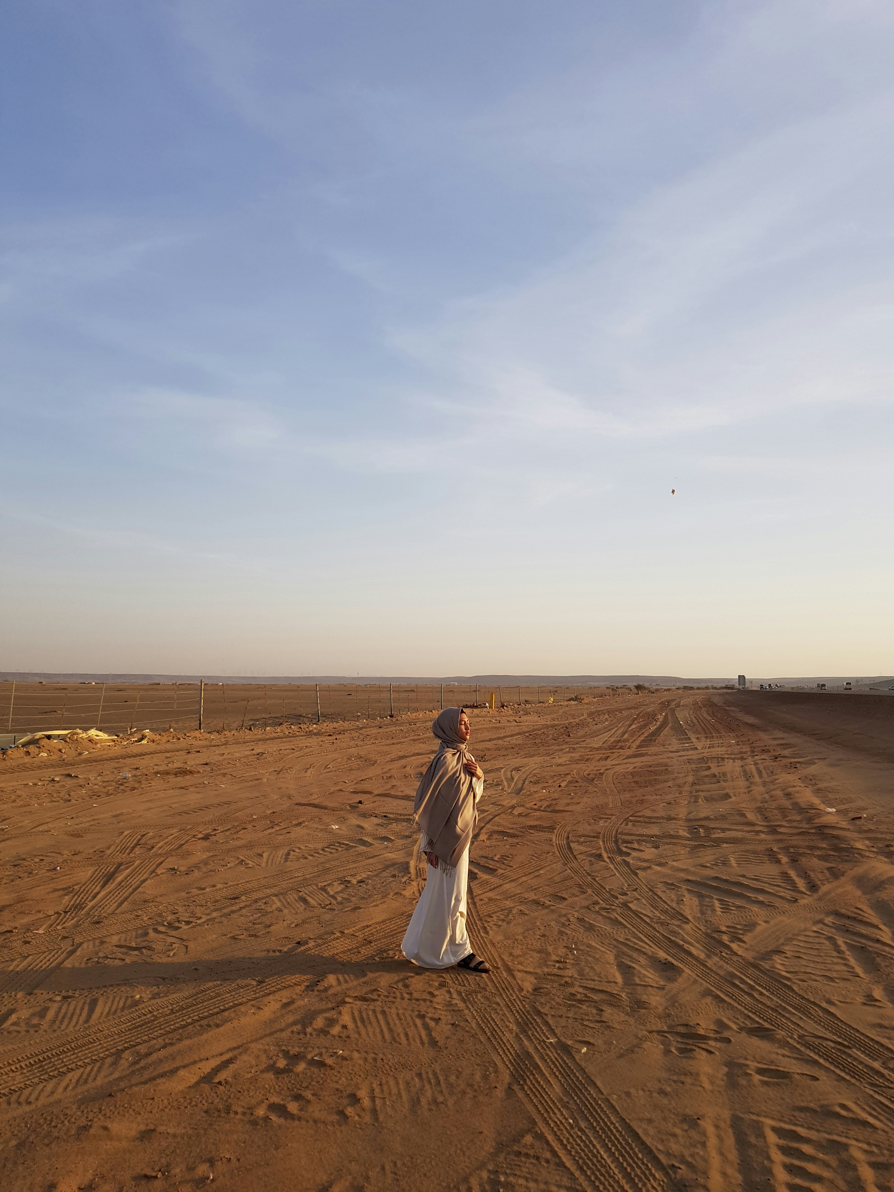 Individual standing on a sandy landscape, gazing upwards towards the sky, with a vast desert backdrop.