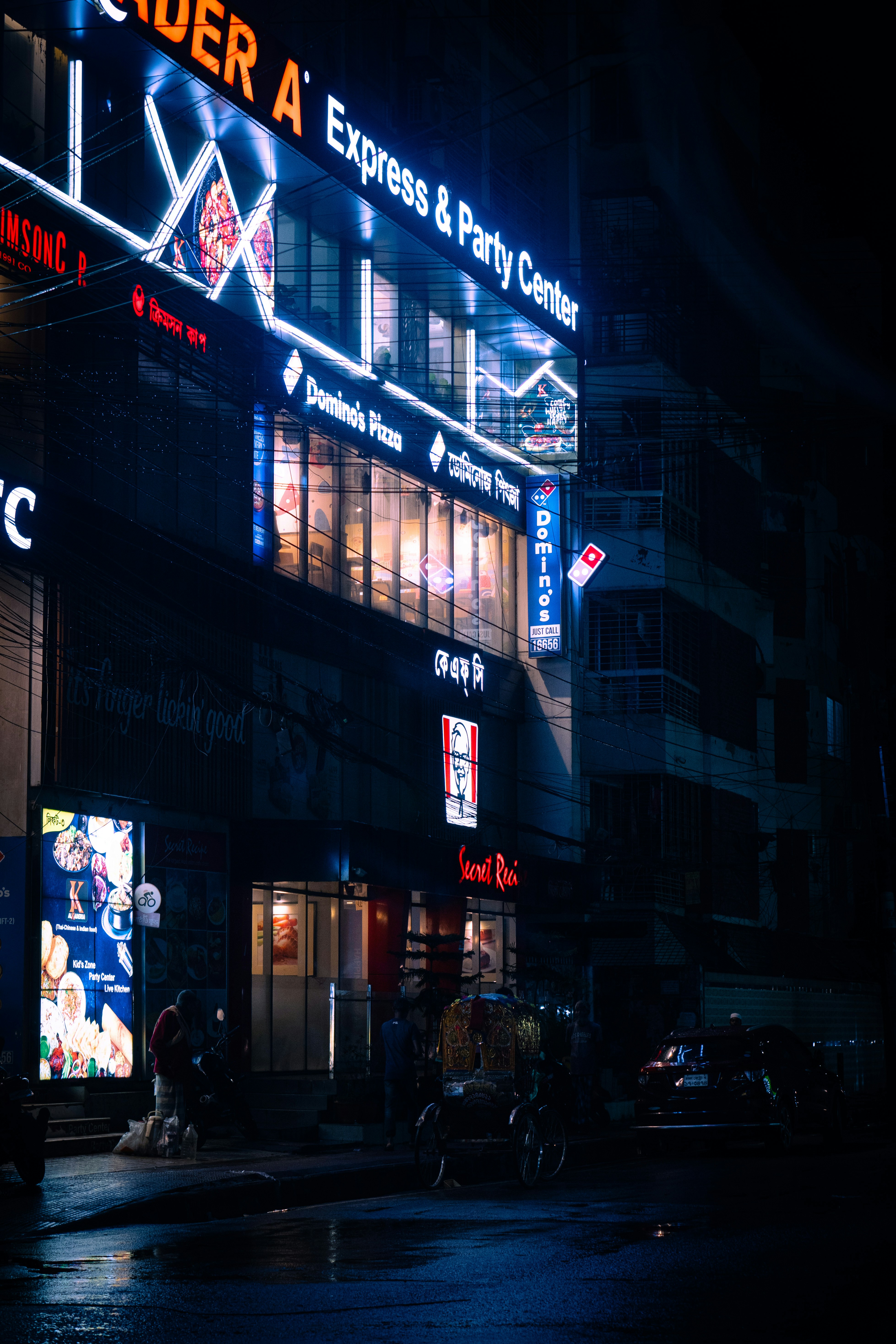 Vibrant storefronts illuminated by neon lights, showcasing popular food brands in an urban setting at night.