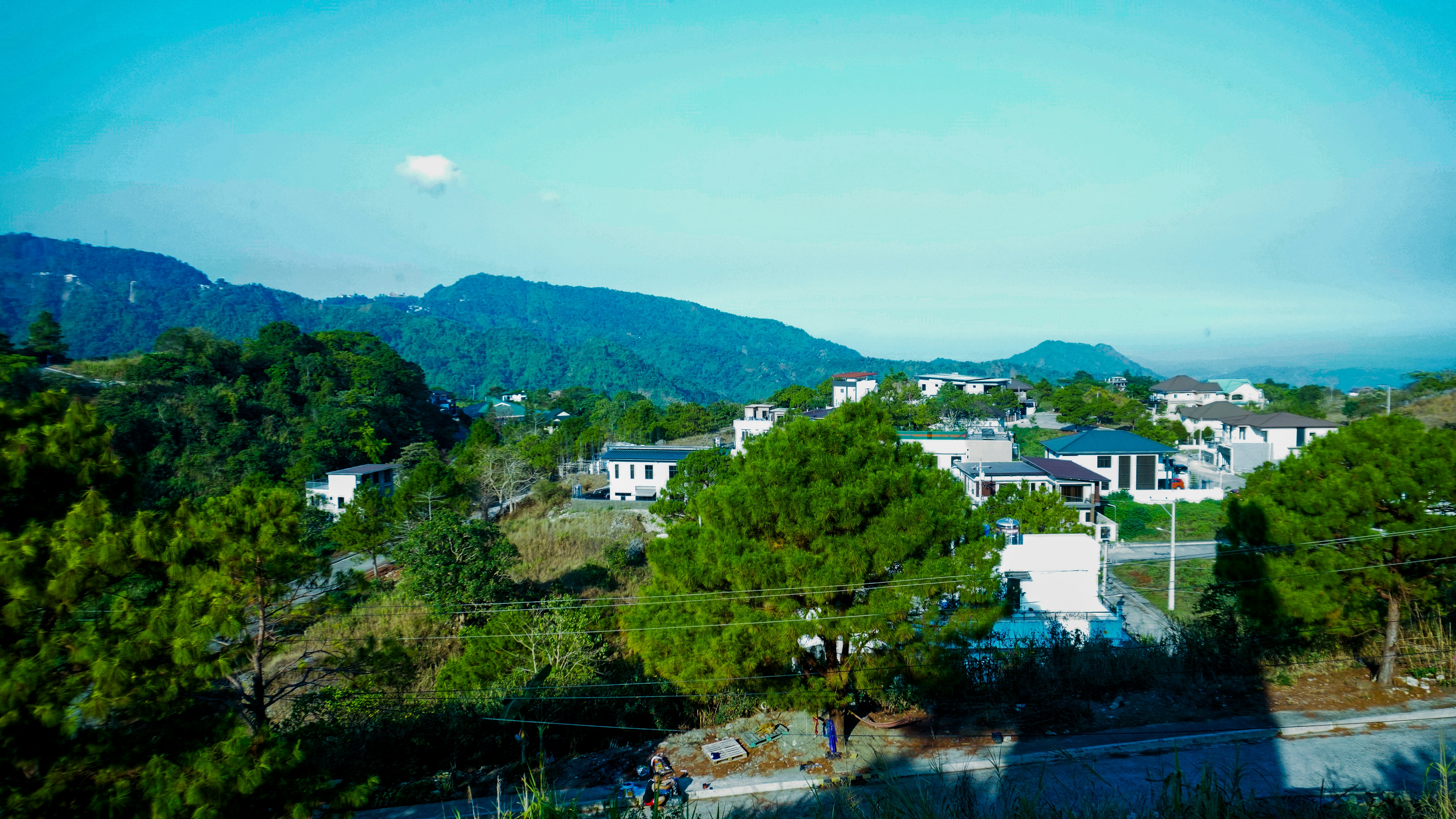 A picturesque view of a hillside community surrounded by lush greenery and distant mountains, showcasing modern architecture and natural beauty.