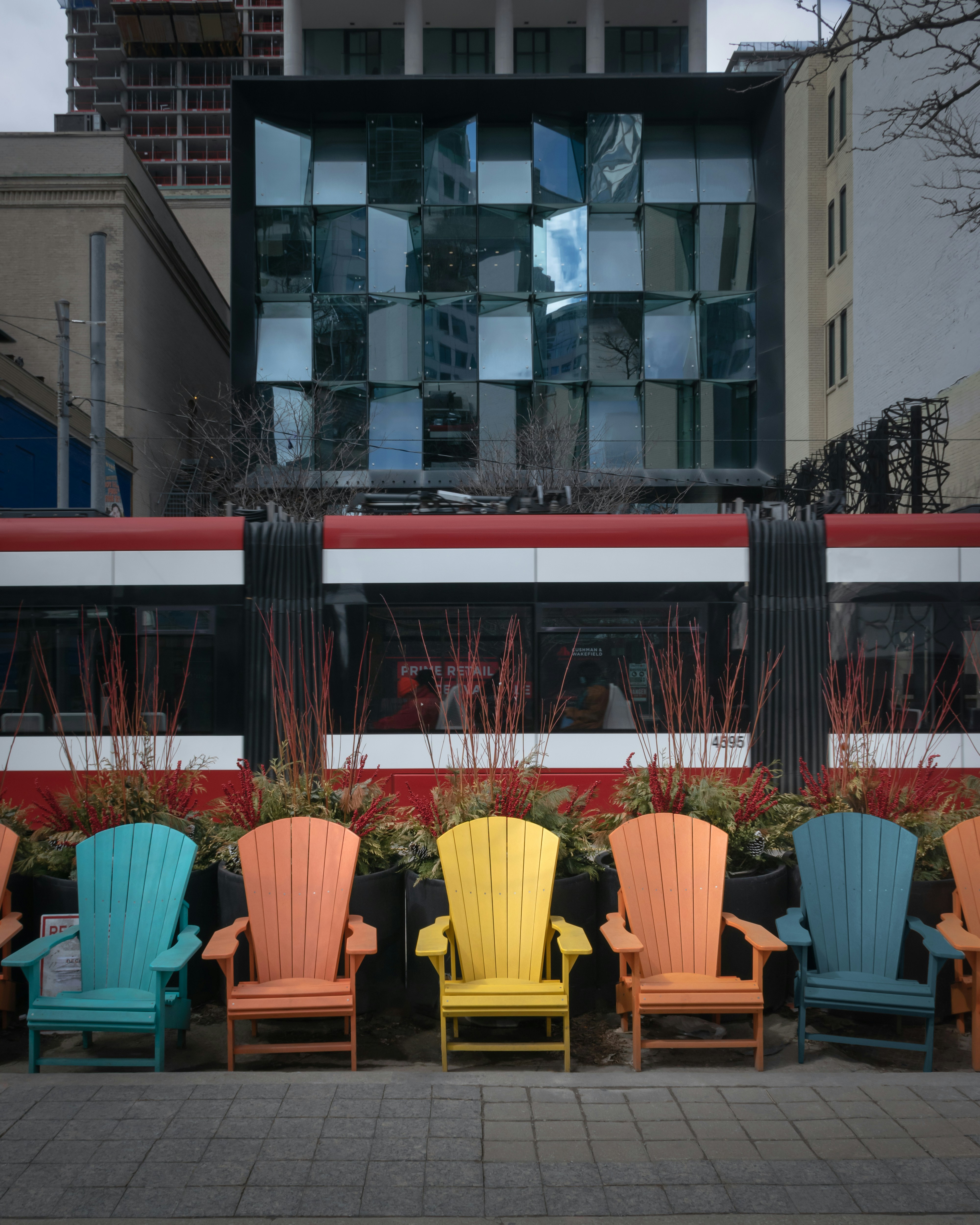 Chromatic Adirondacks Align: Colorful Chairs Framing a Glass Urban Facade