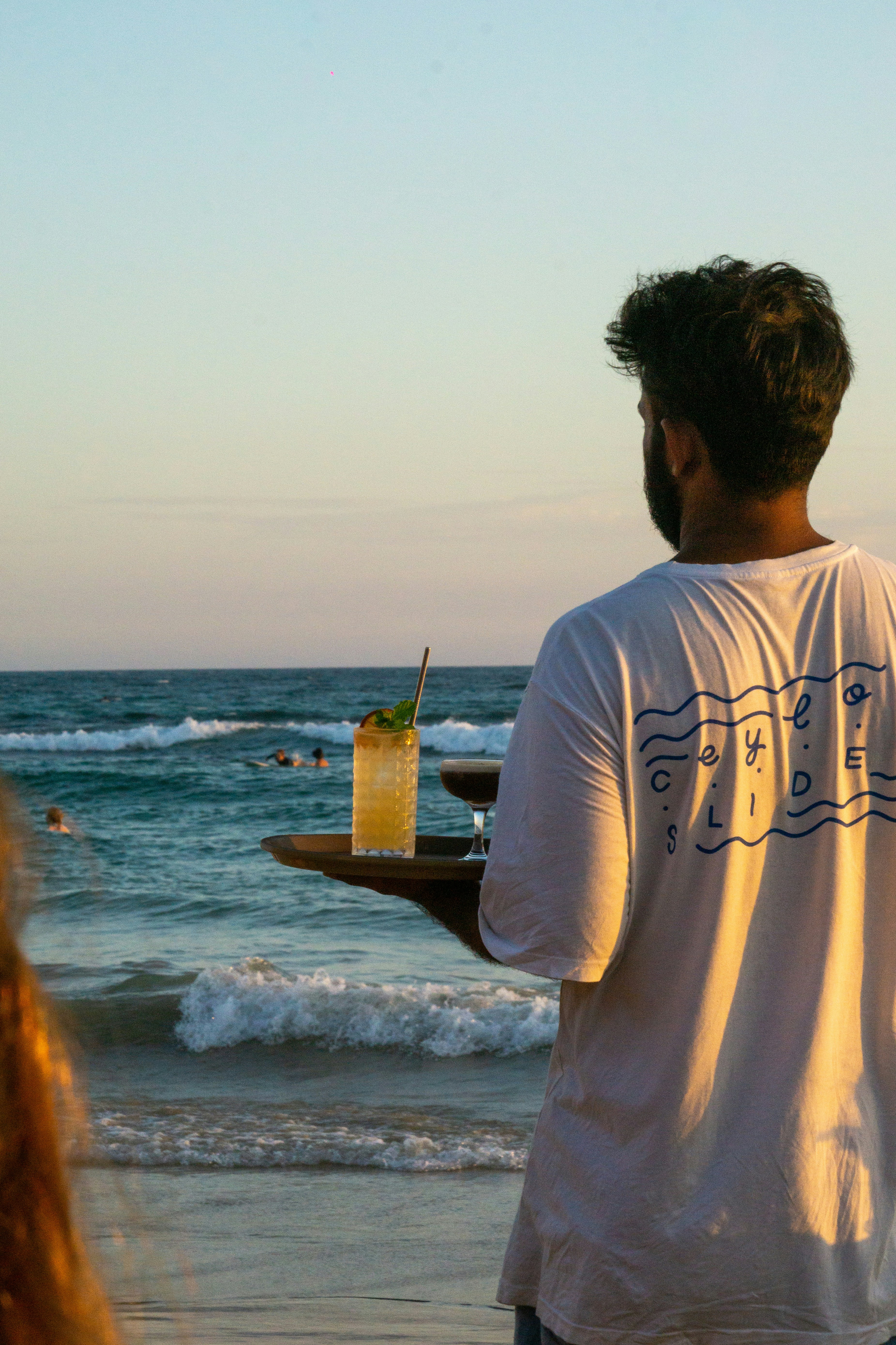 Dusk on Deck: A Beachside Server Balances Drinks Against the Atlantic Glow