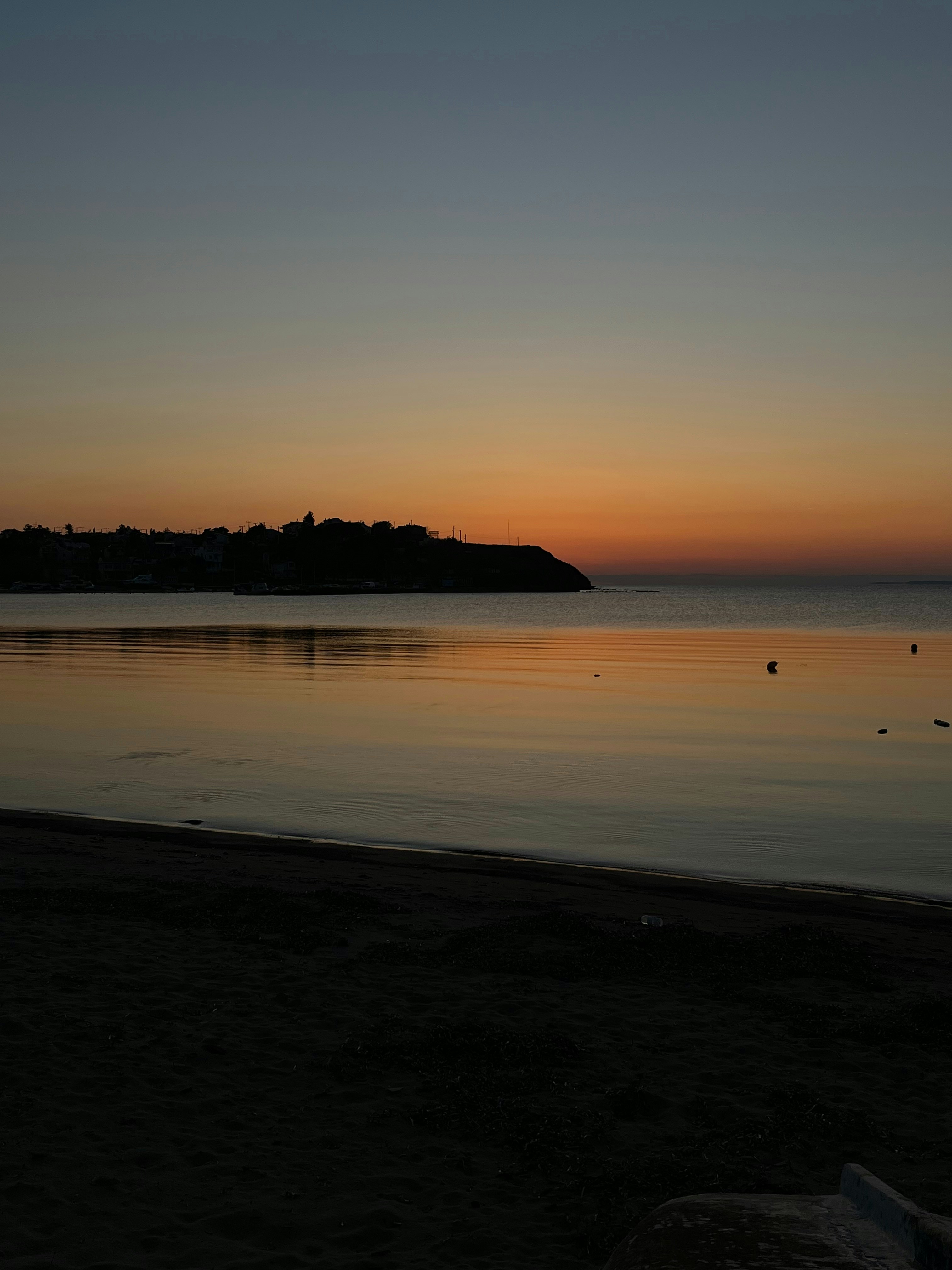 Quiet beach at sunset with a silhouette of distant hills against a gradient sky.