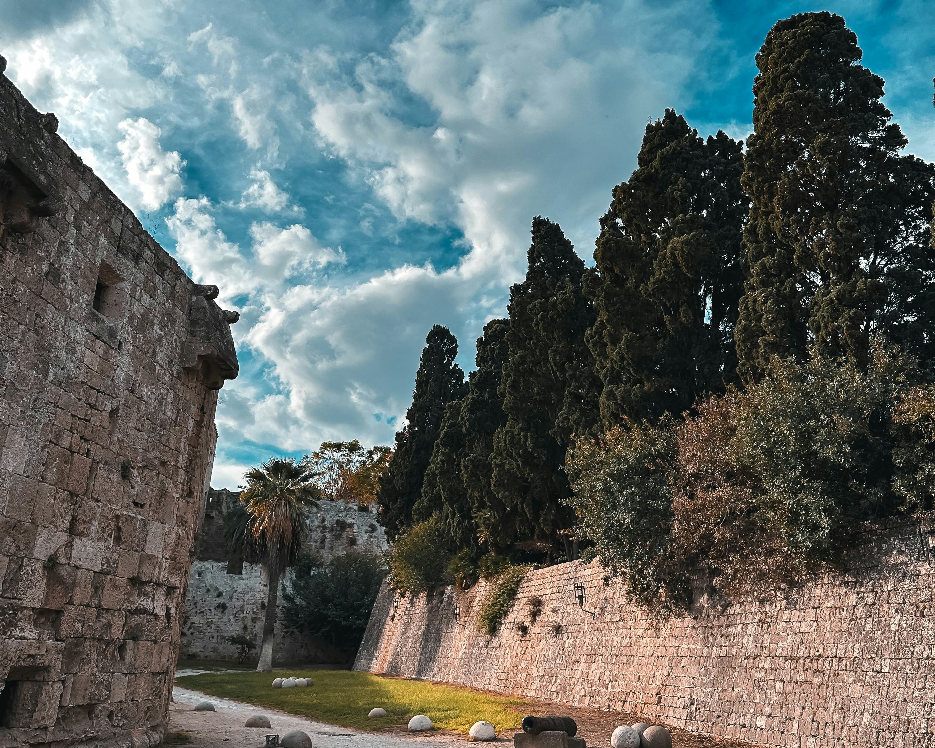 Sunlit Corridor Between Ancient Walls and Towering Evergreens