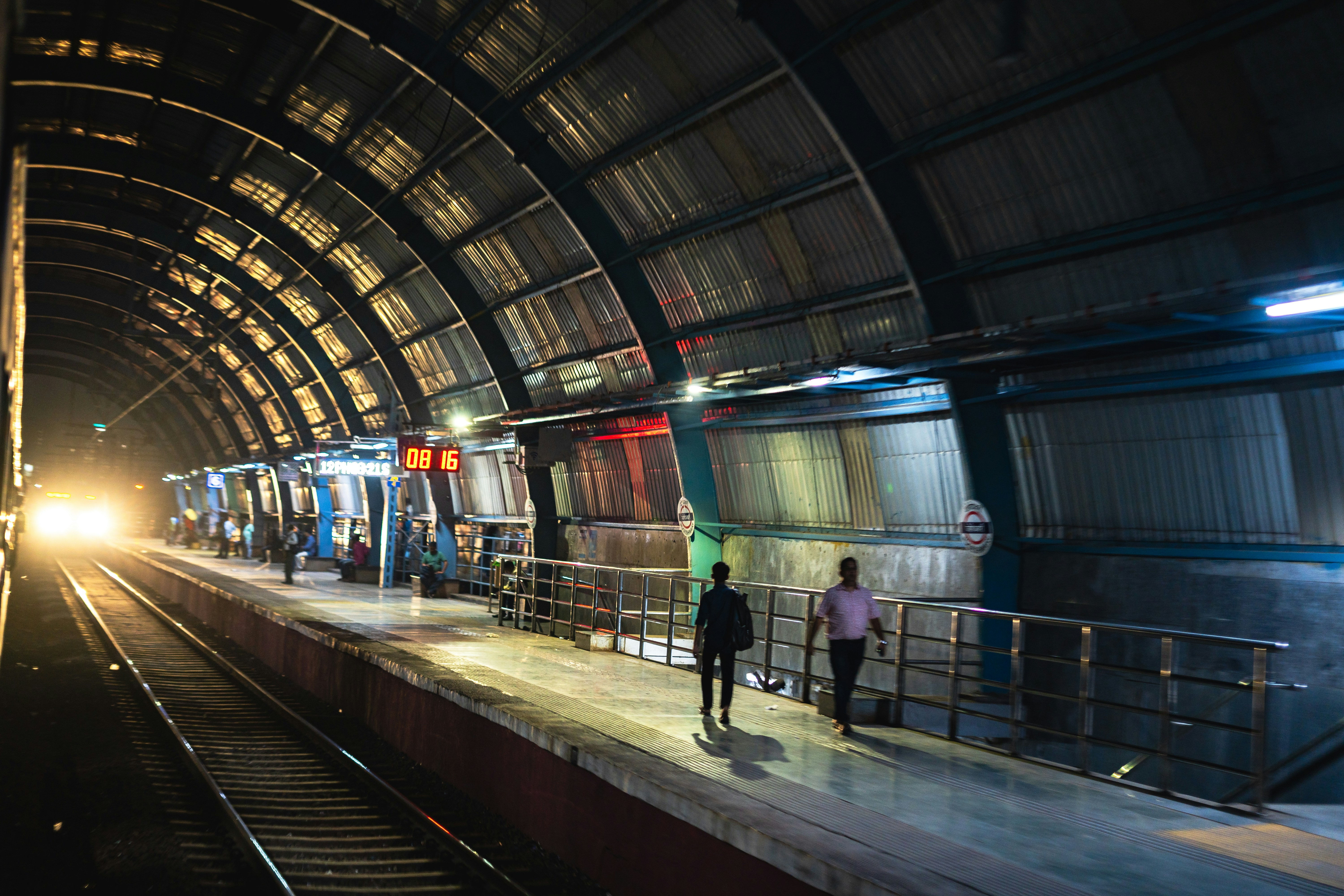 Curved Silence: Two Pedestrians on a Neon-Blue Subway Platform