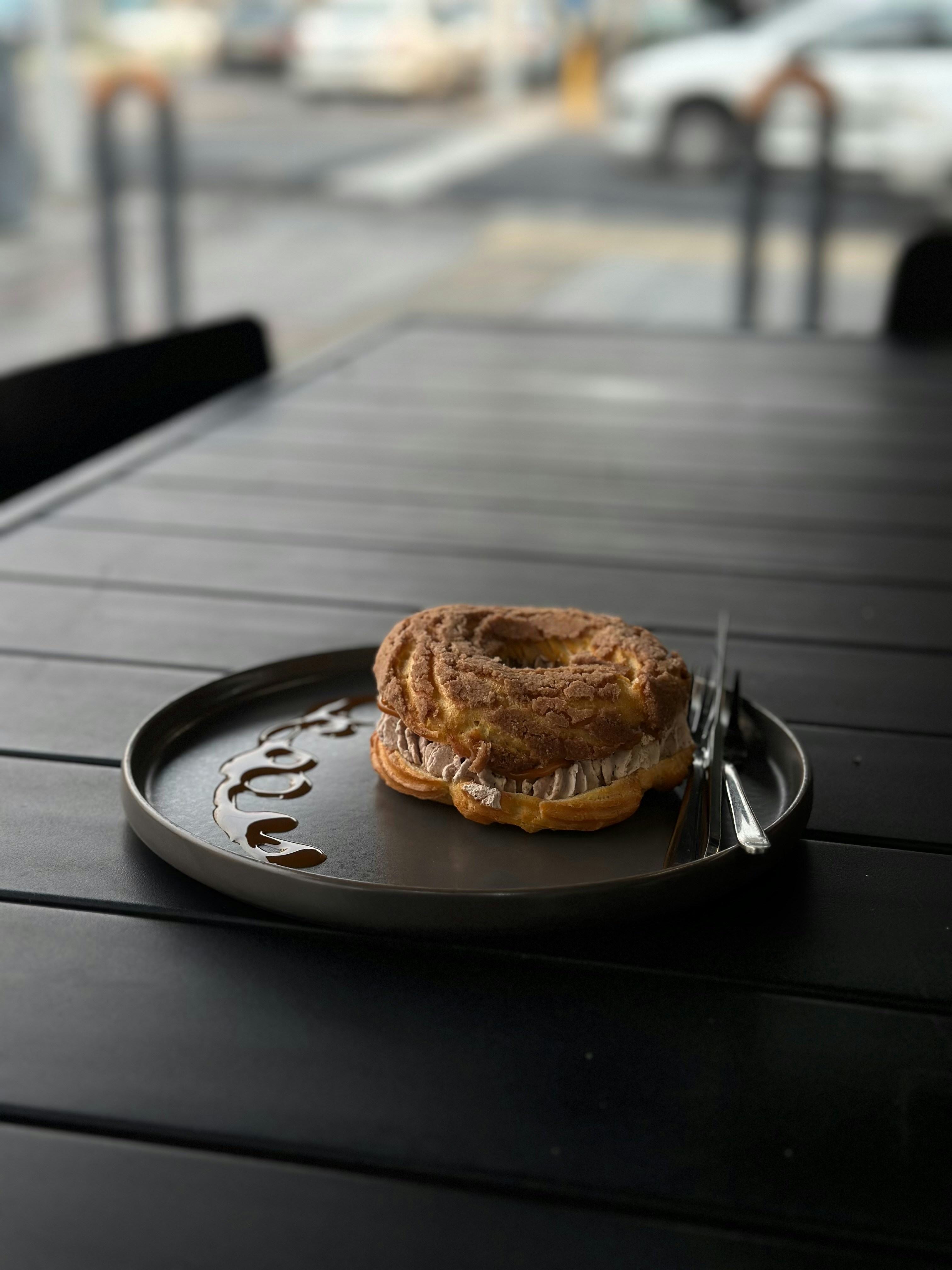 A donut sitting on top of a black plate on a table photo – Free Cutlery ...
