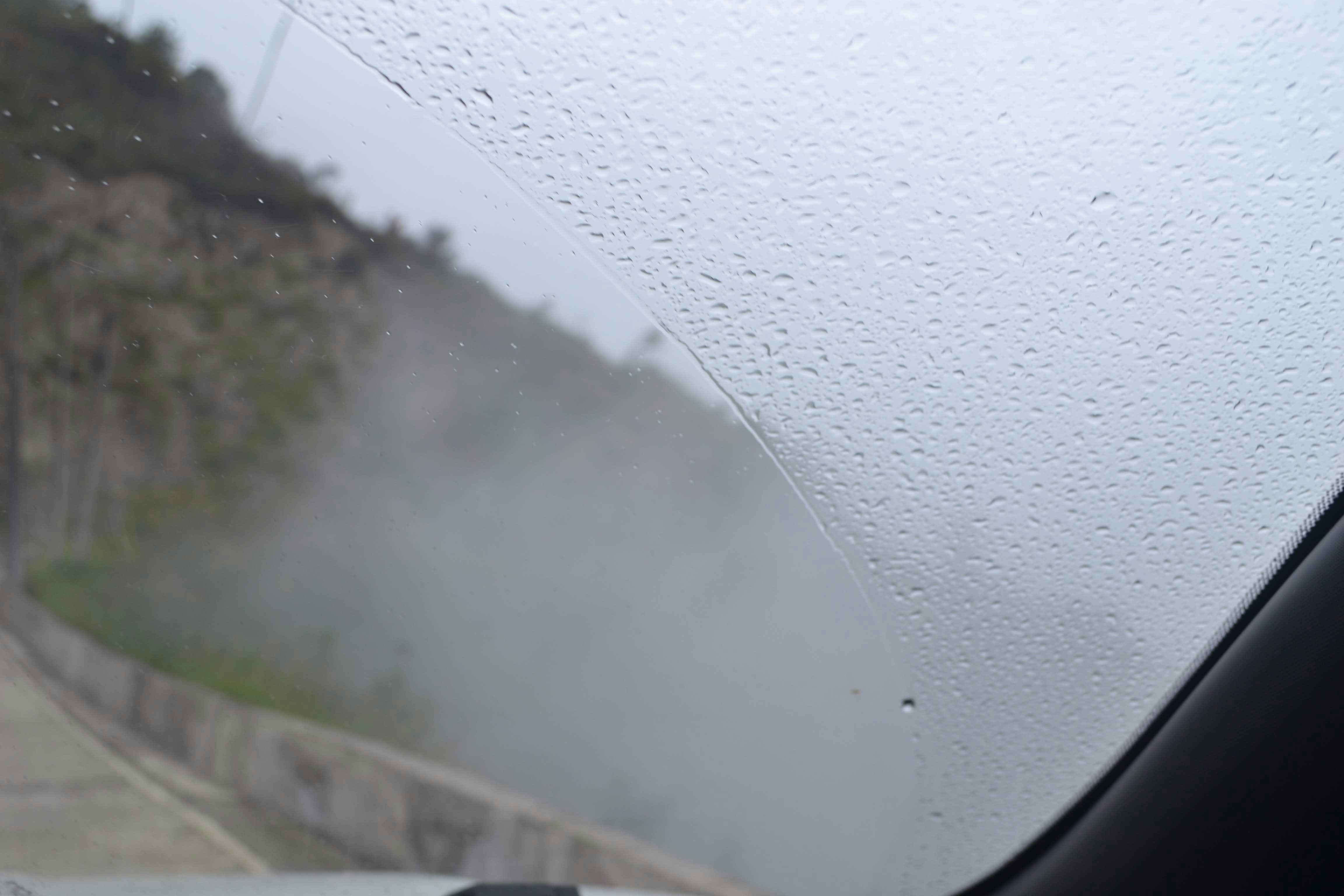 Raindrops on a car window with a foggy mountain cliff in the background.