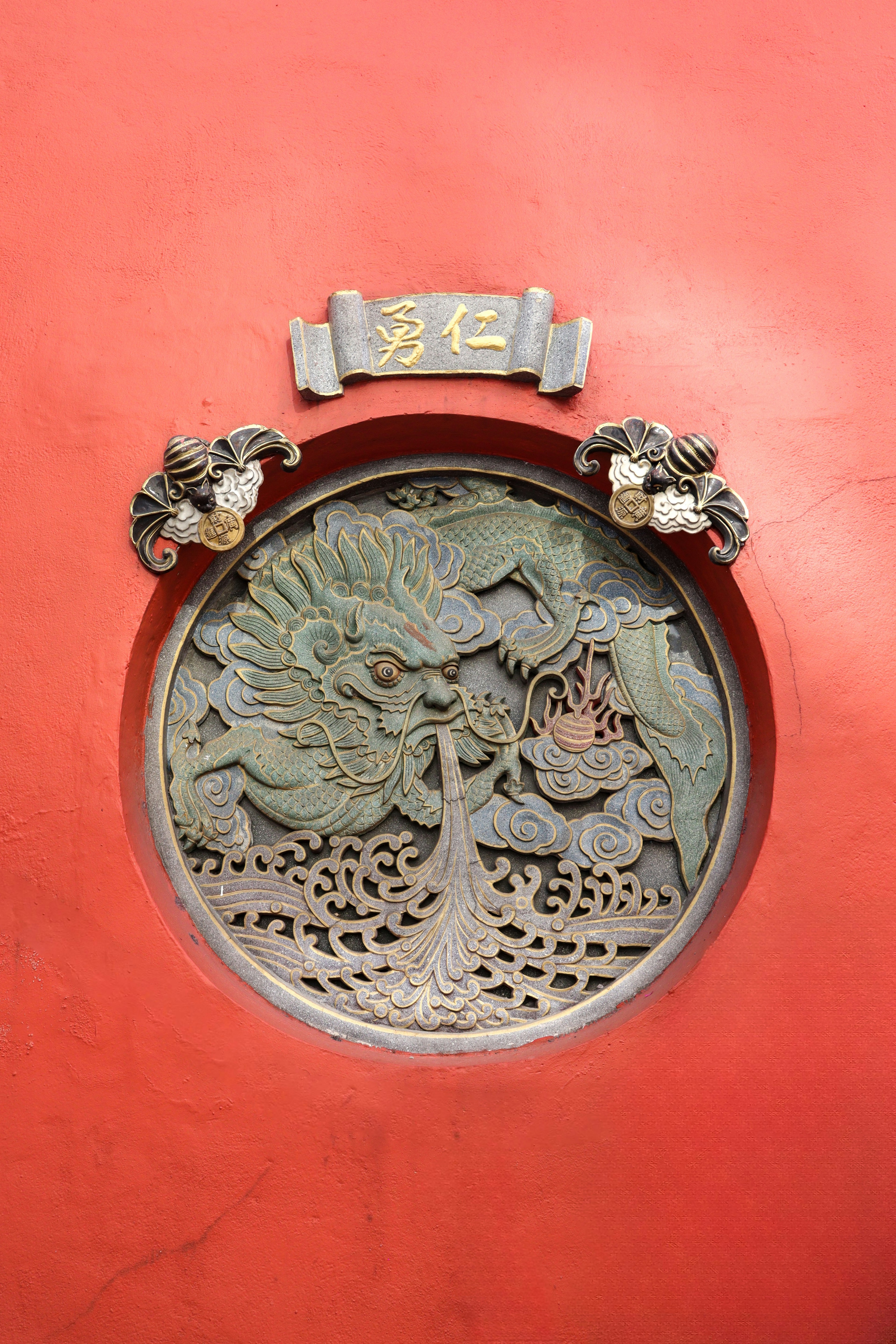 Crimson Dragon Relief: A Circular Metal Carving on a Red Wall