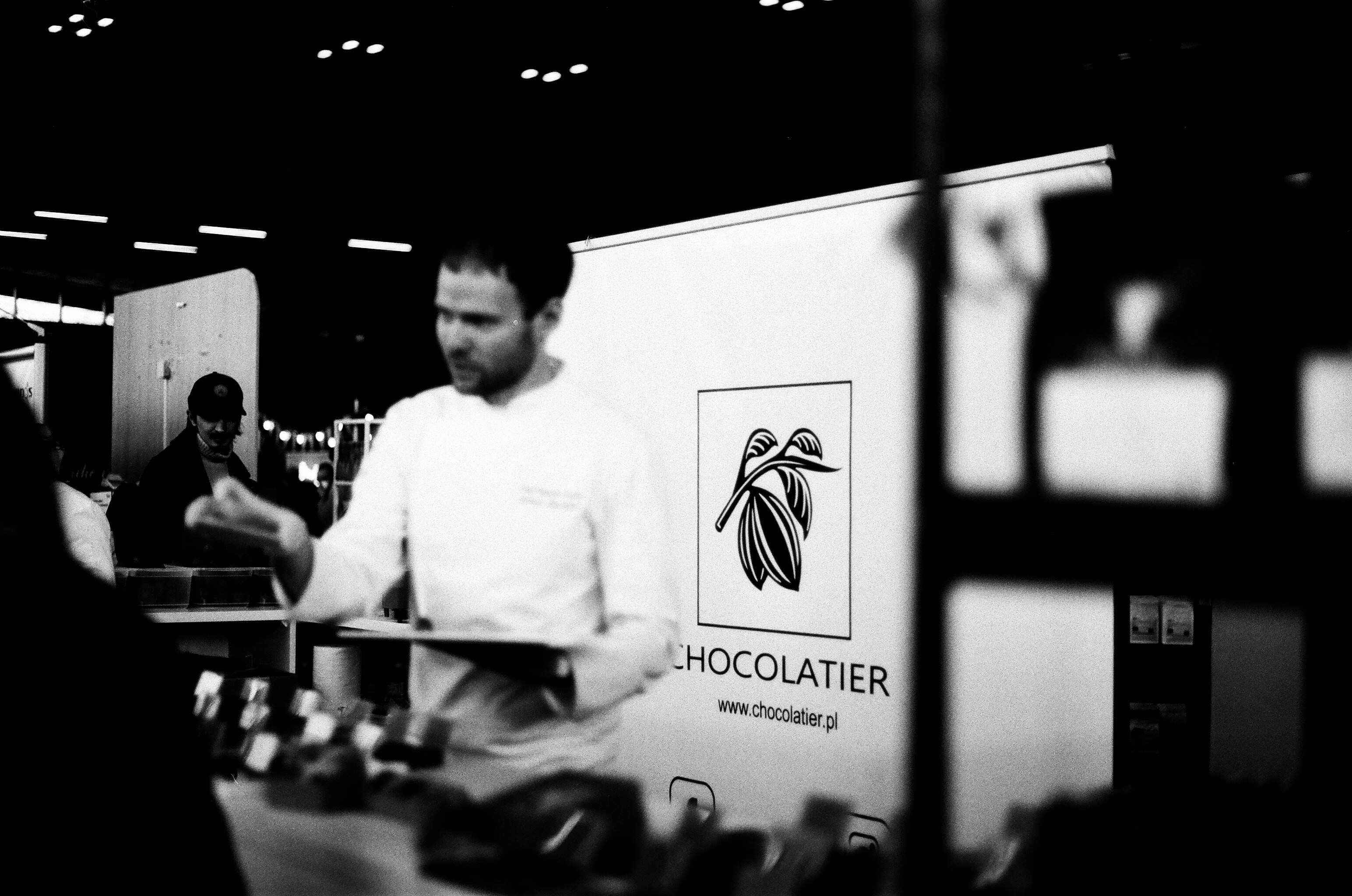 Black and white scene of a chocolatier presenting sweets at a market stall.