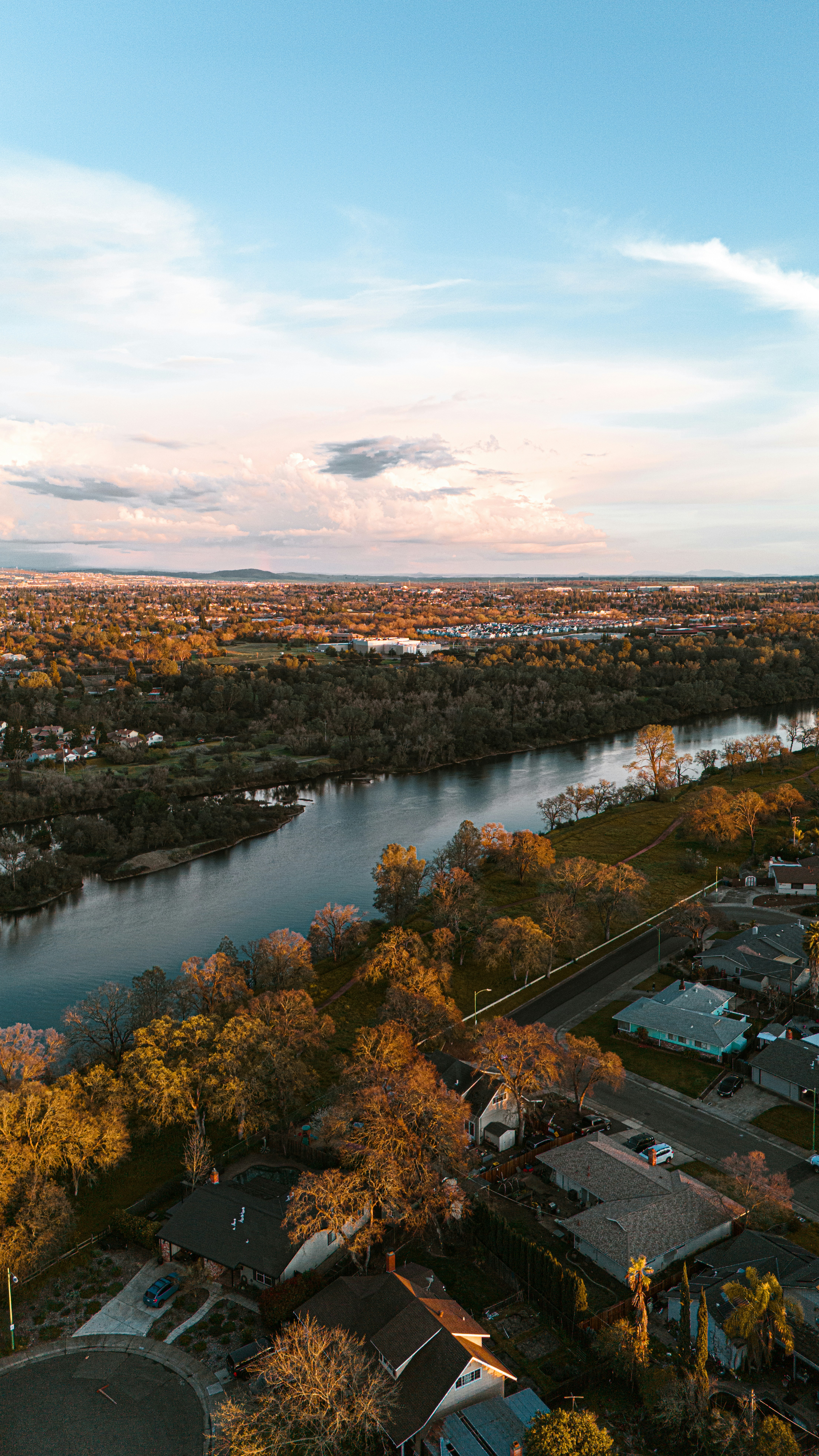 Aerial view of a serene river winding through a suburban landscape at sunset.
