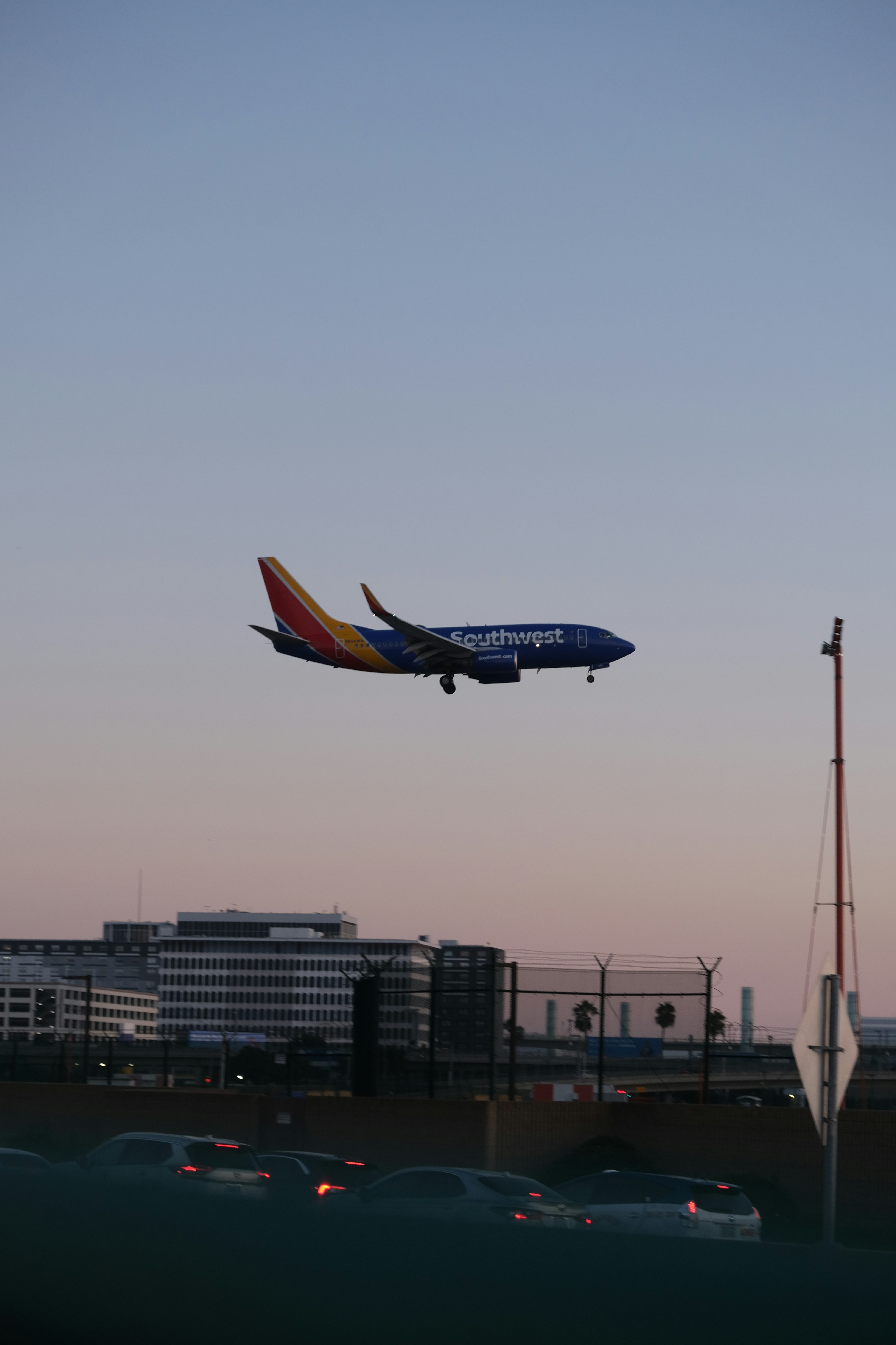 Southwest Airlines aircraft descending towards the runway as the sun sets, with urban buildings in the background.