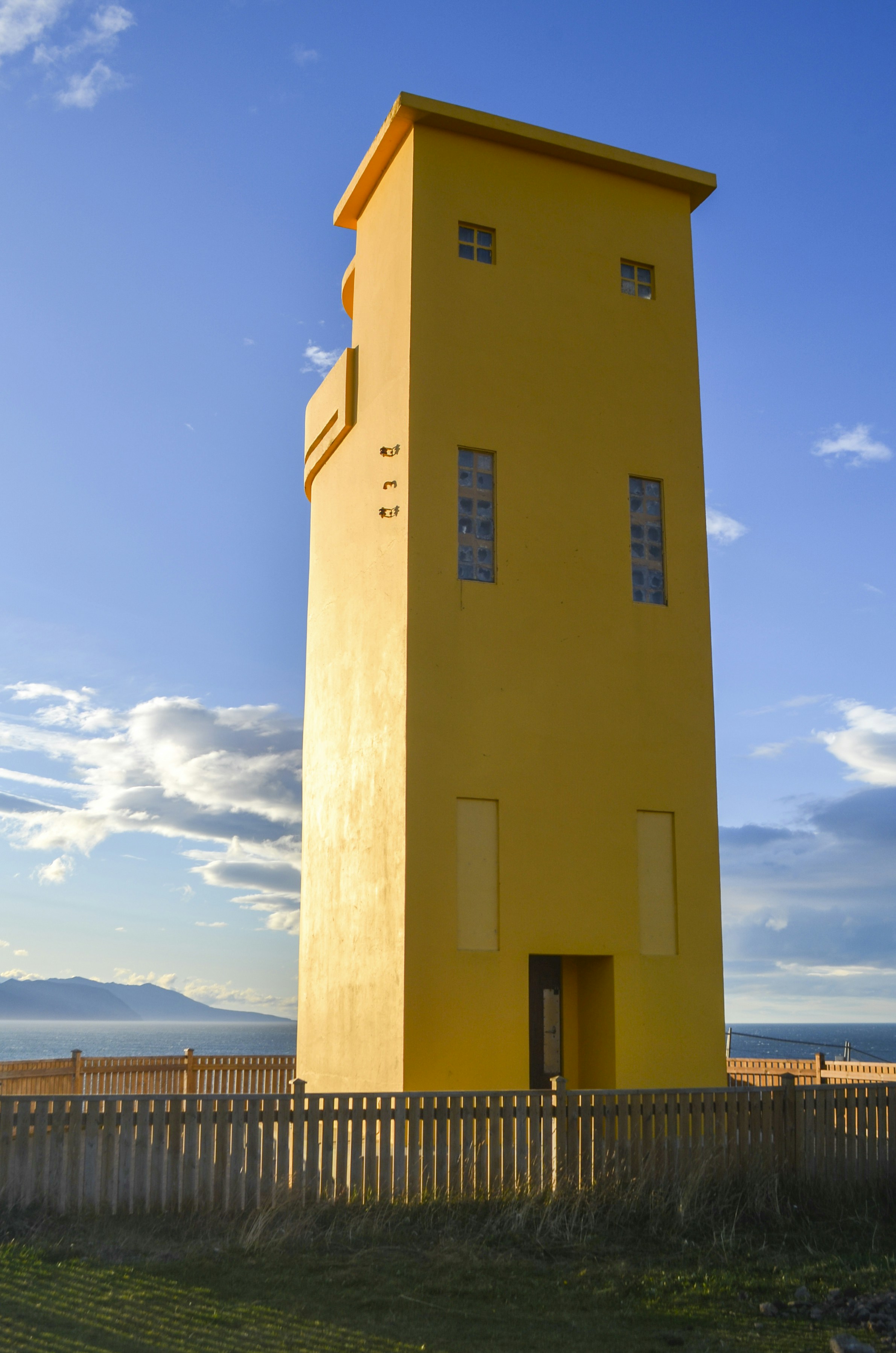 A tall yellow building sitting on top of a lush green field photo ...