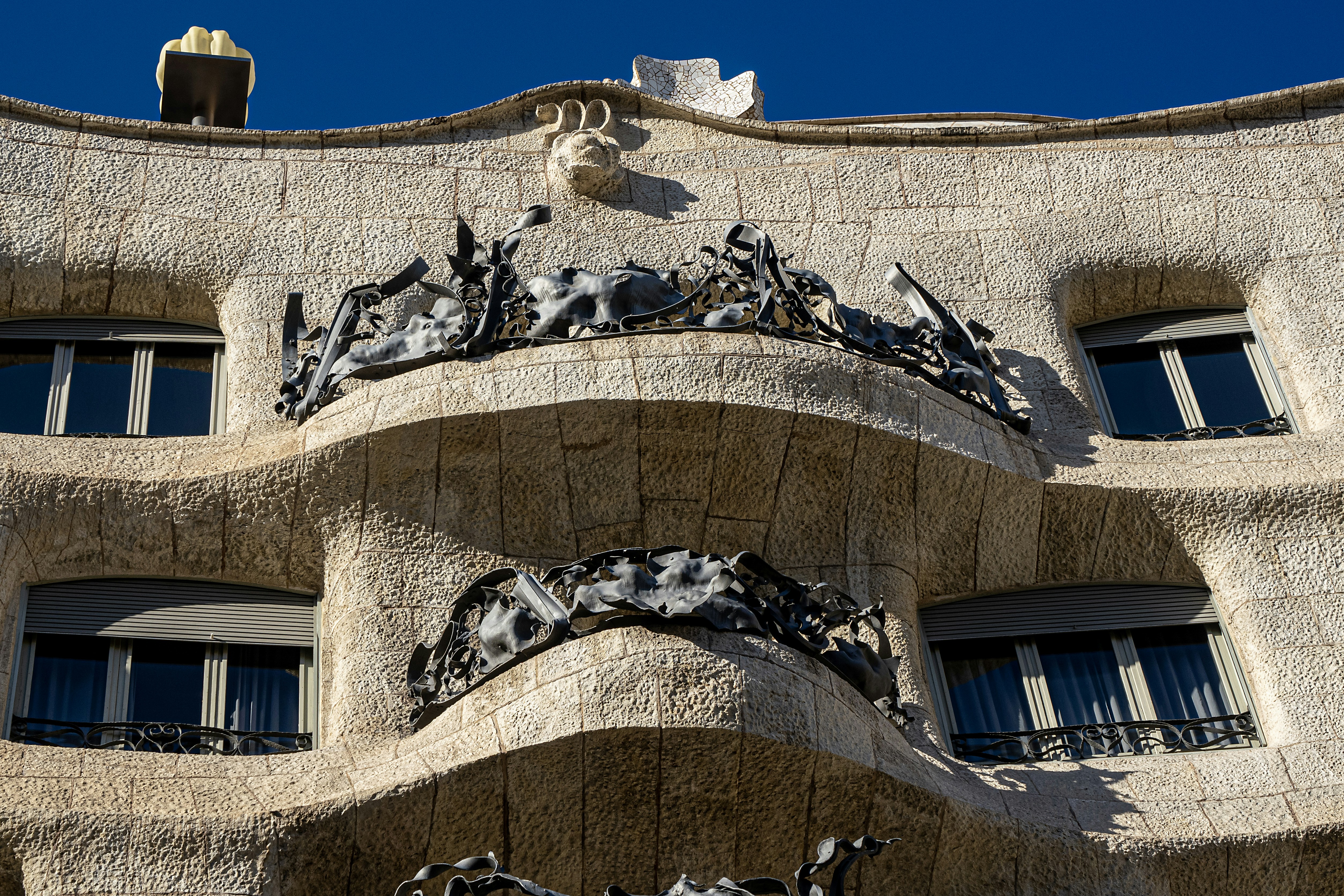 Gaudí-Inspired Stone Relief Above Curved Balconies on a Sunlit Façade
