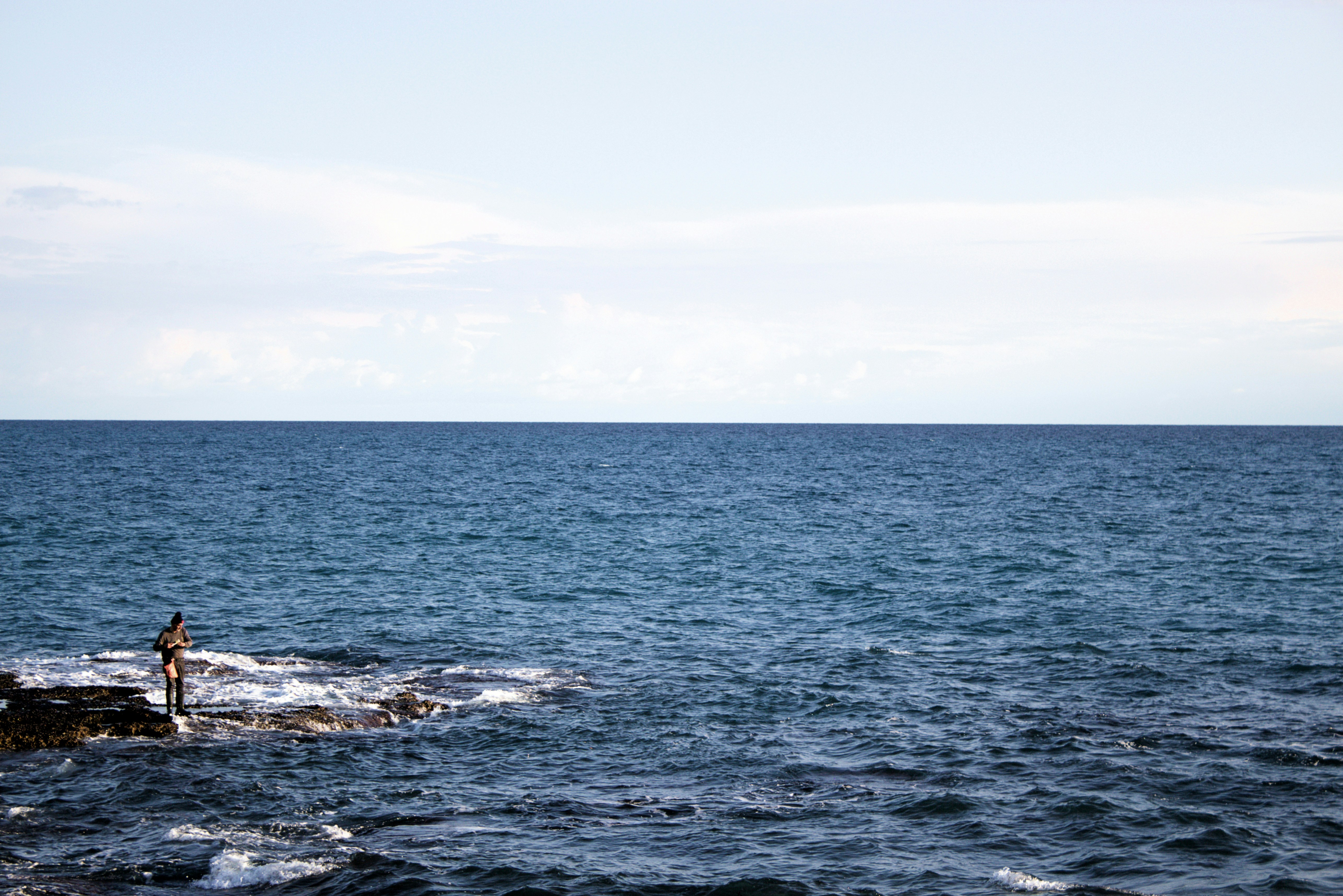 A man standing on top of a rock next to the ocean photo – Free Sea ...