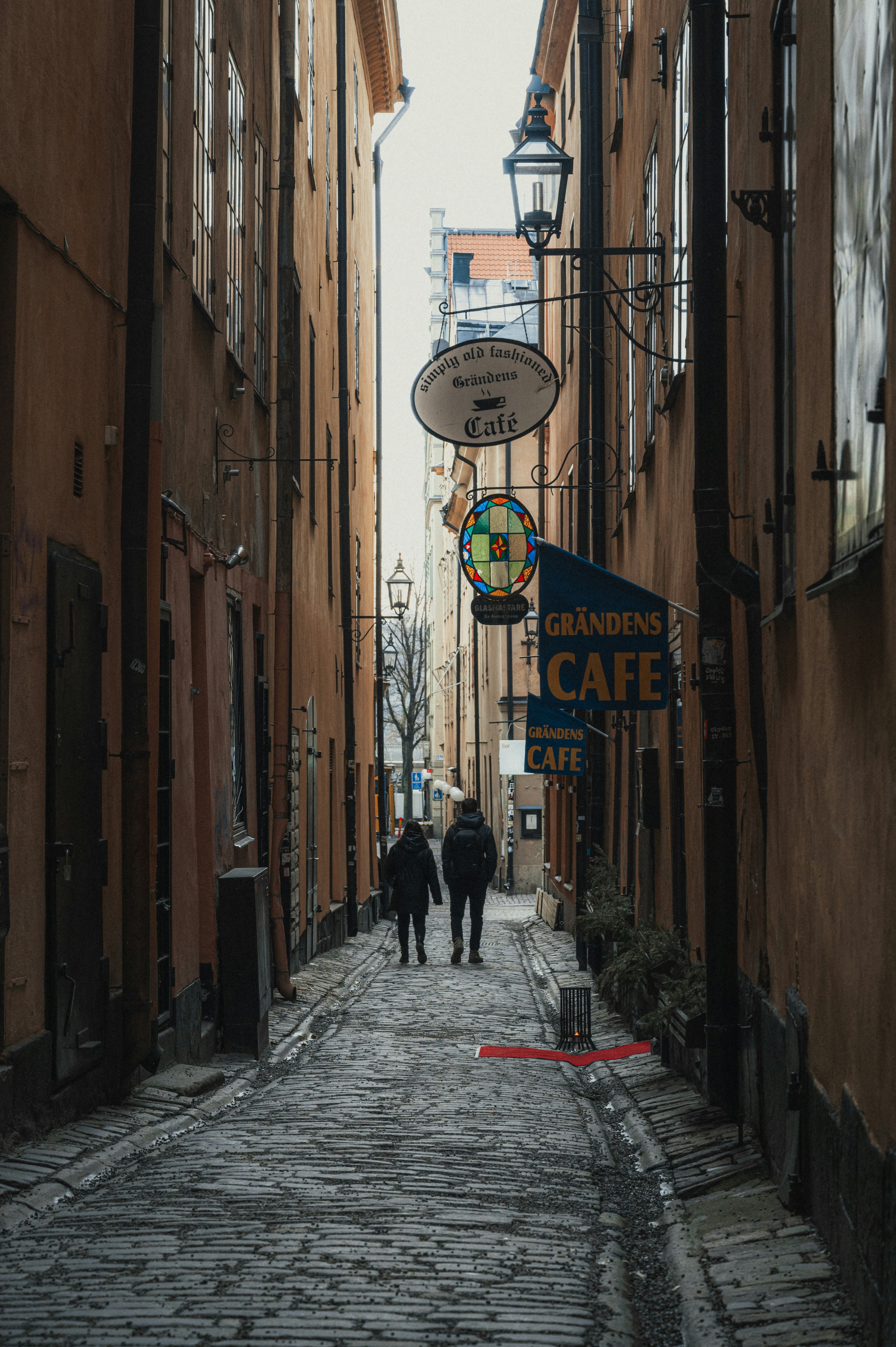 Quiet Cobblestone Alley Framed by Café Signs and Two Figures