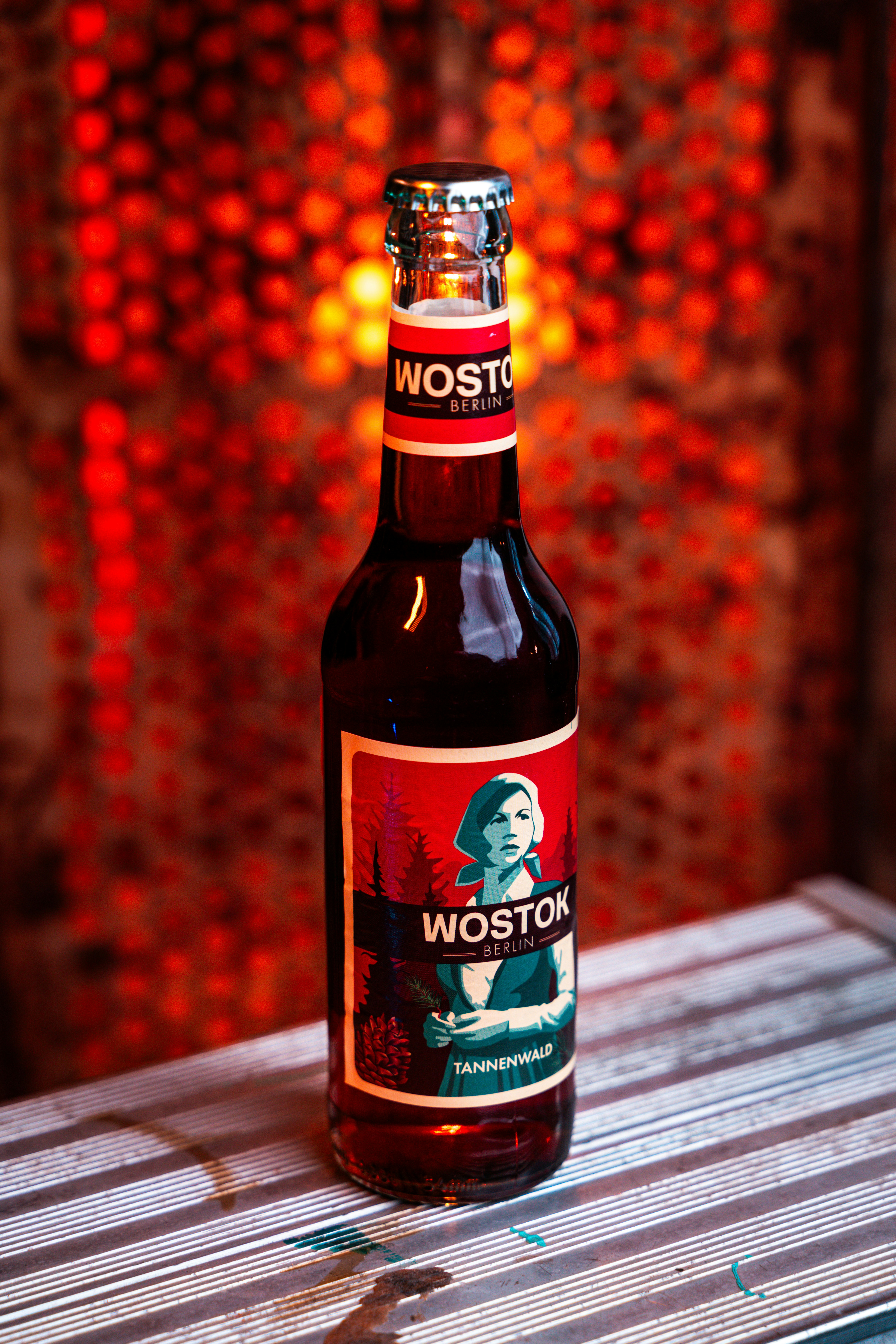 WOSTOK's Tannenwald flavor lights up with a bokeh of red, celebrating the moment on a rustic table.