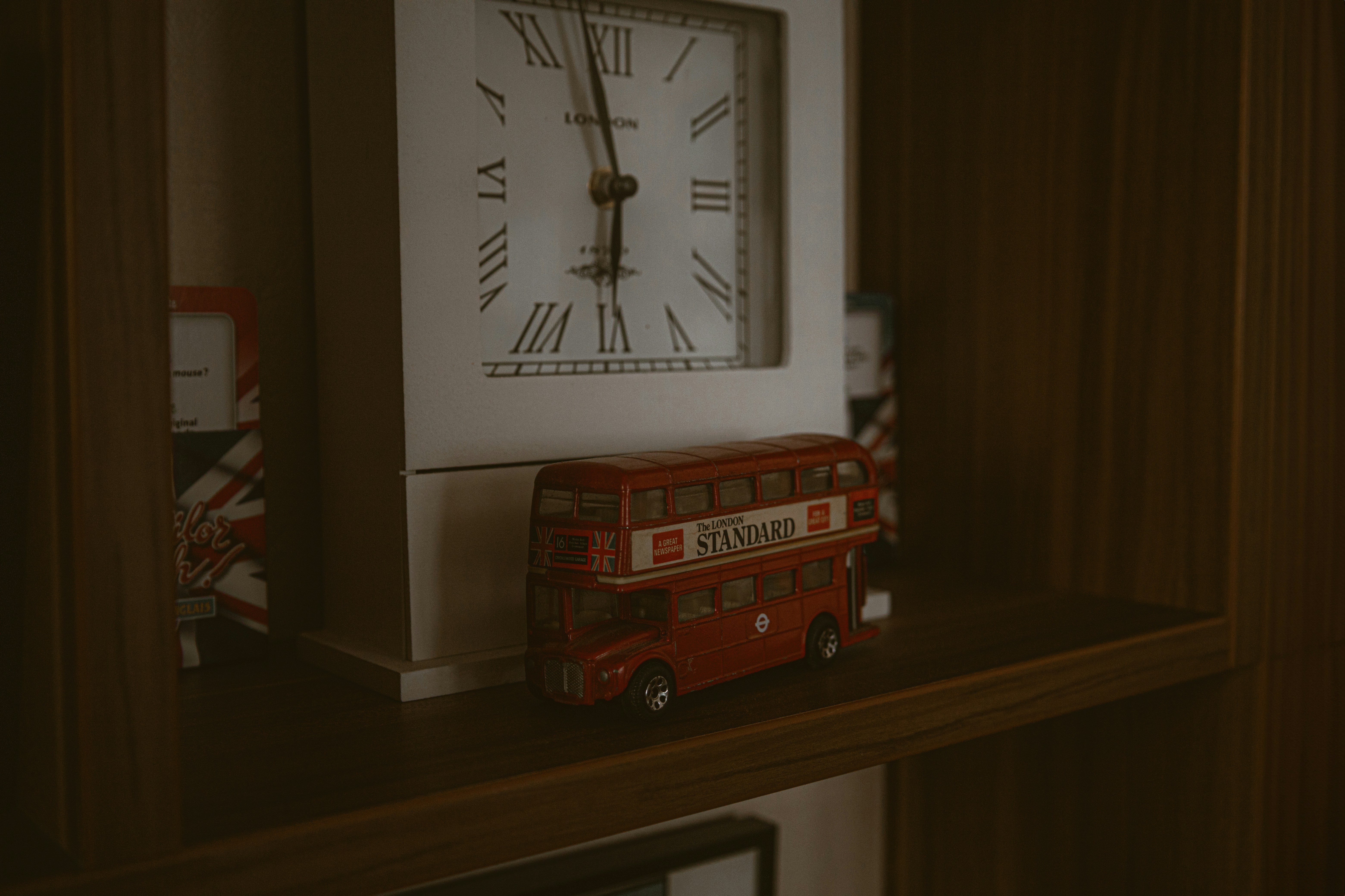 Timekeeper on a Wooden Shelf: A Red London Bus Beneath a Clock