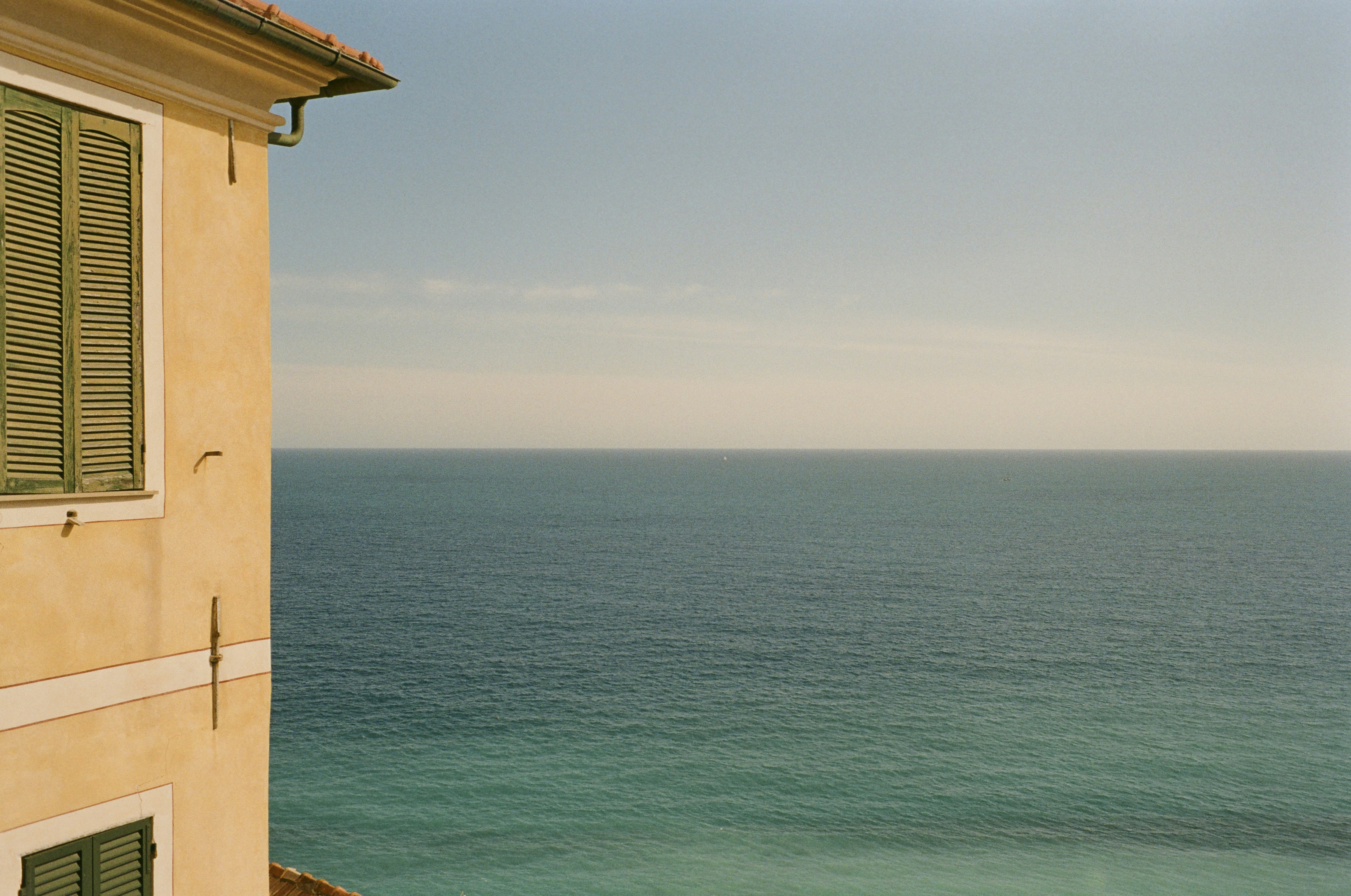 Building facade with a shuttered window overlooking the expansive Ligurian Sea under a clear sky.