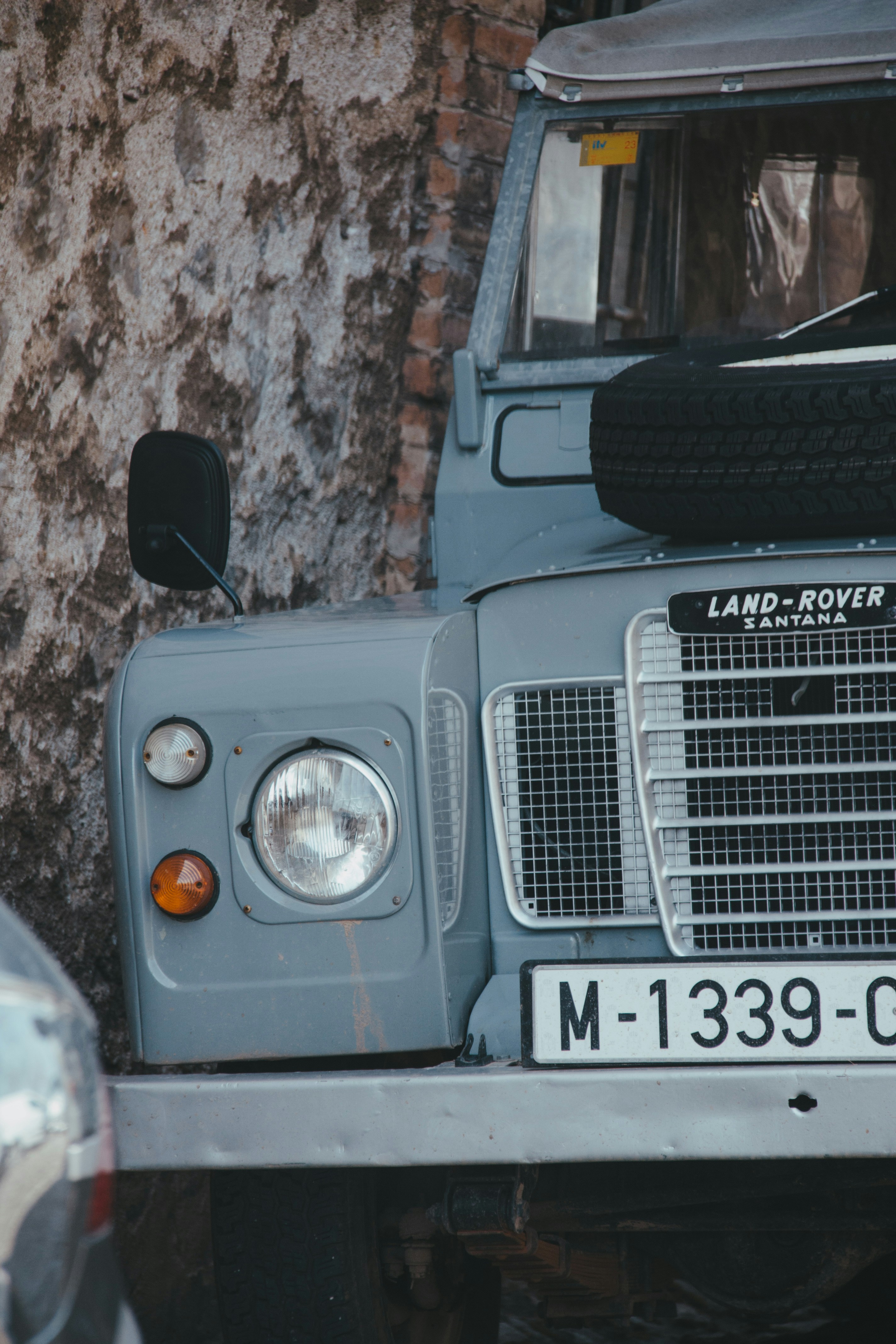 Weathered Blue Land Rover Santana: Grille, Headlight, and Brick Wall Portrait
